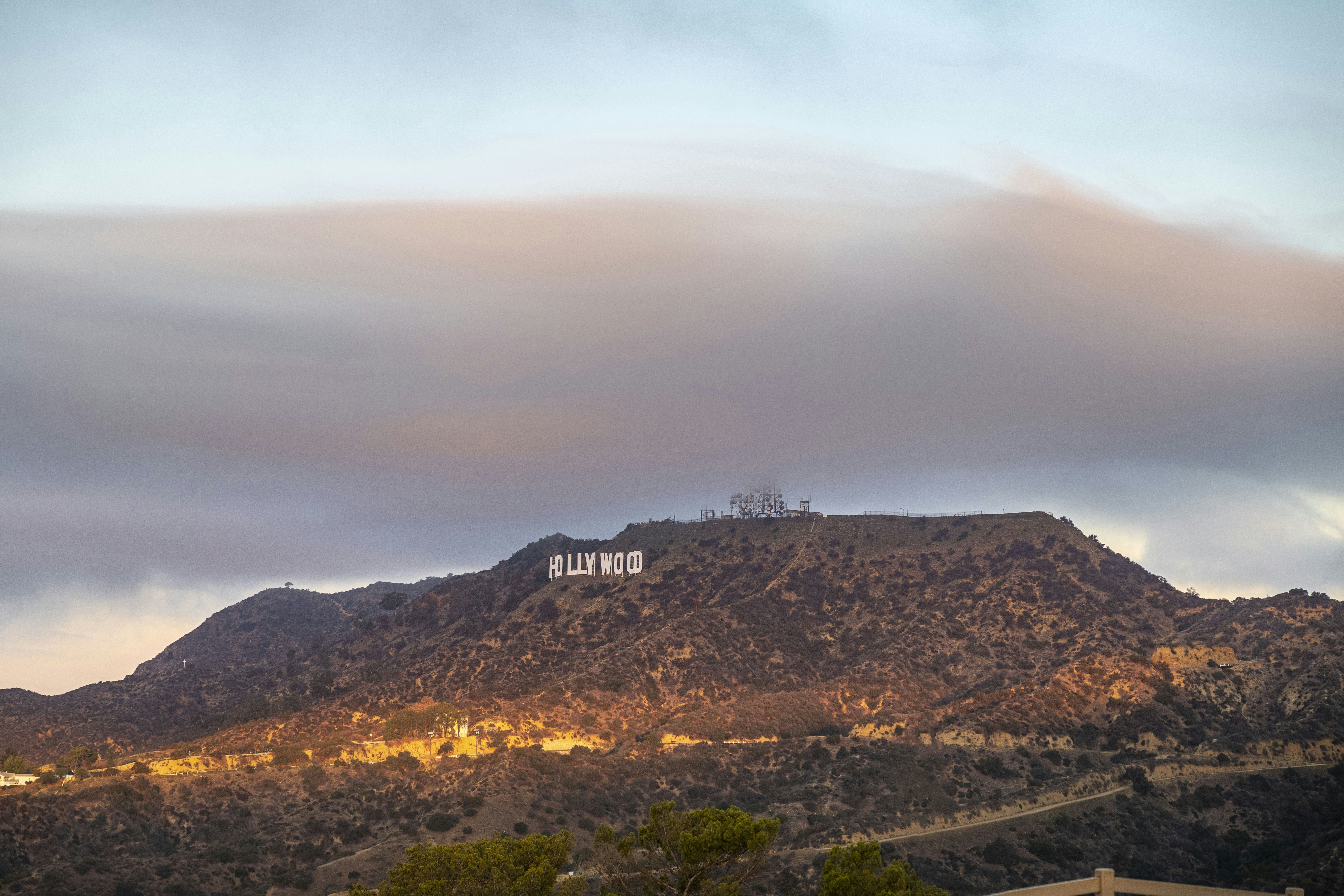 Hollywood sign perched on a sunlit hill, surrounded by soft clouds and rugged terrain.