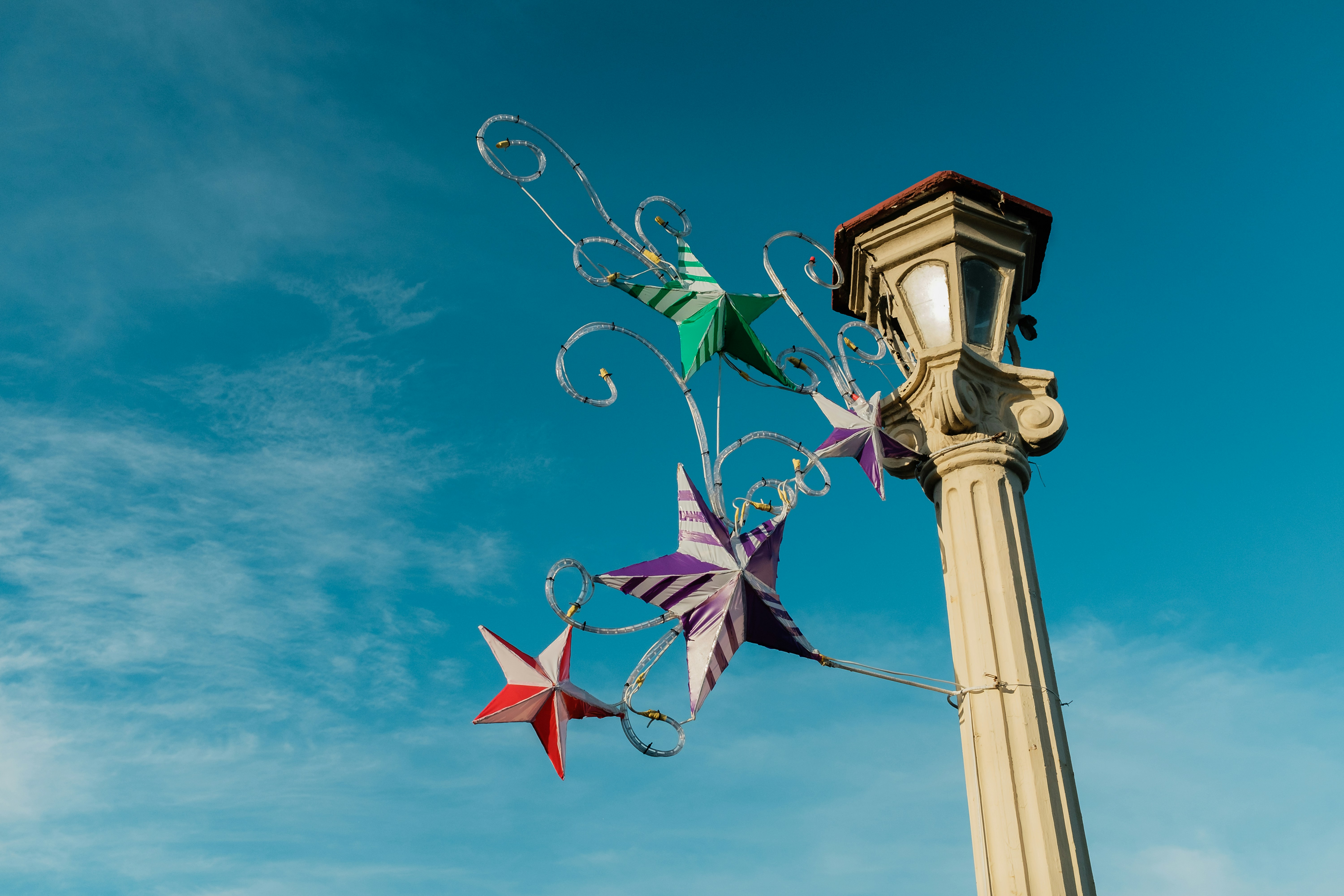 Ornate street lamp topped with colorful star decorations against a clear blue sky.
