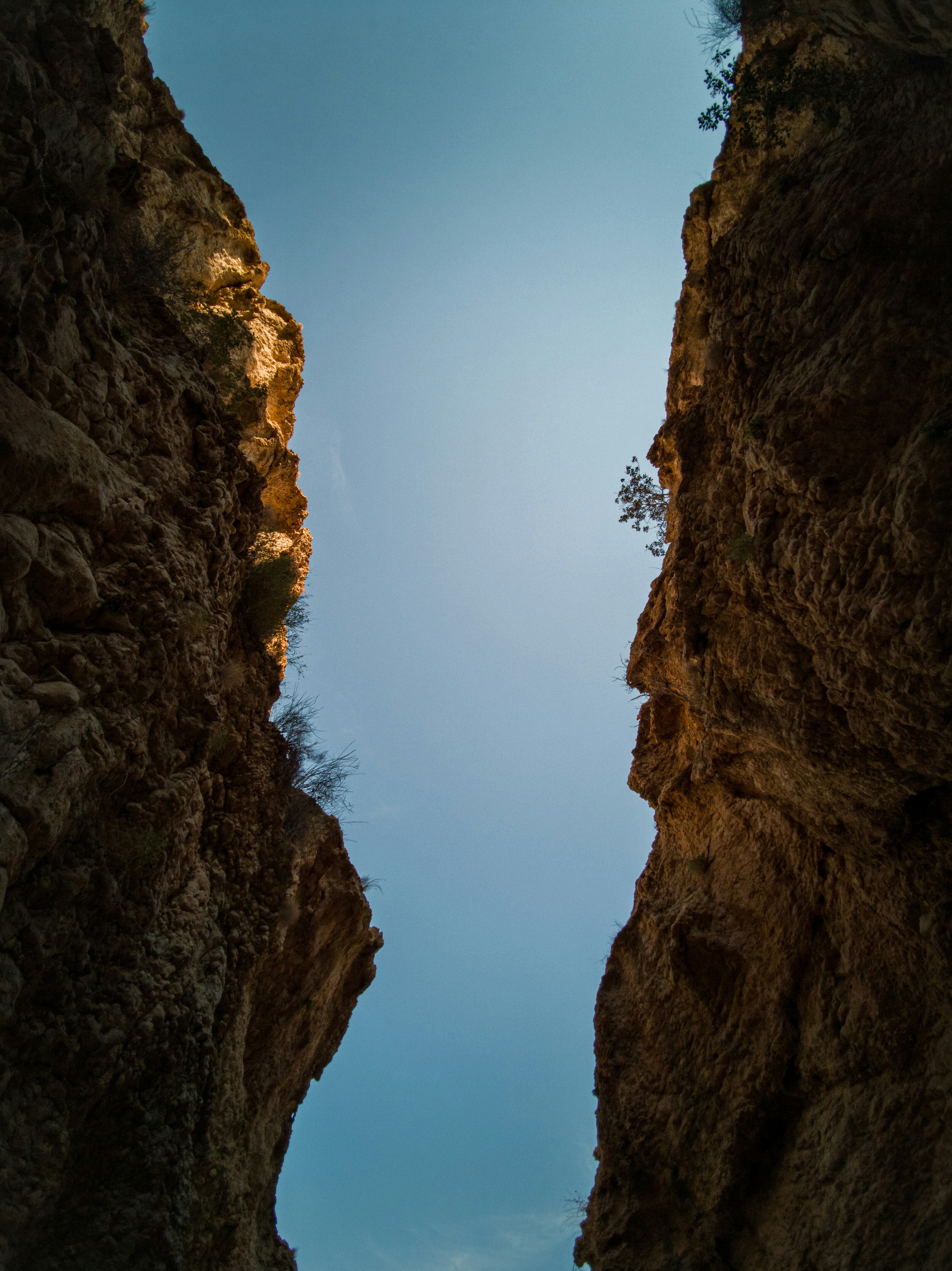 Narrow canyon walls framing a clear blue sky, highlighting the natural erosion process. Sunlight illuminates the rocky textures.