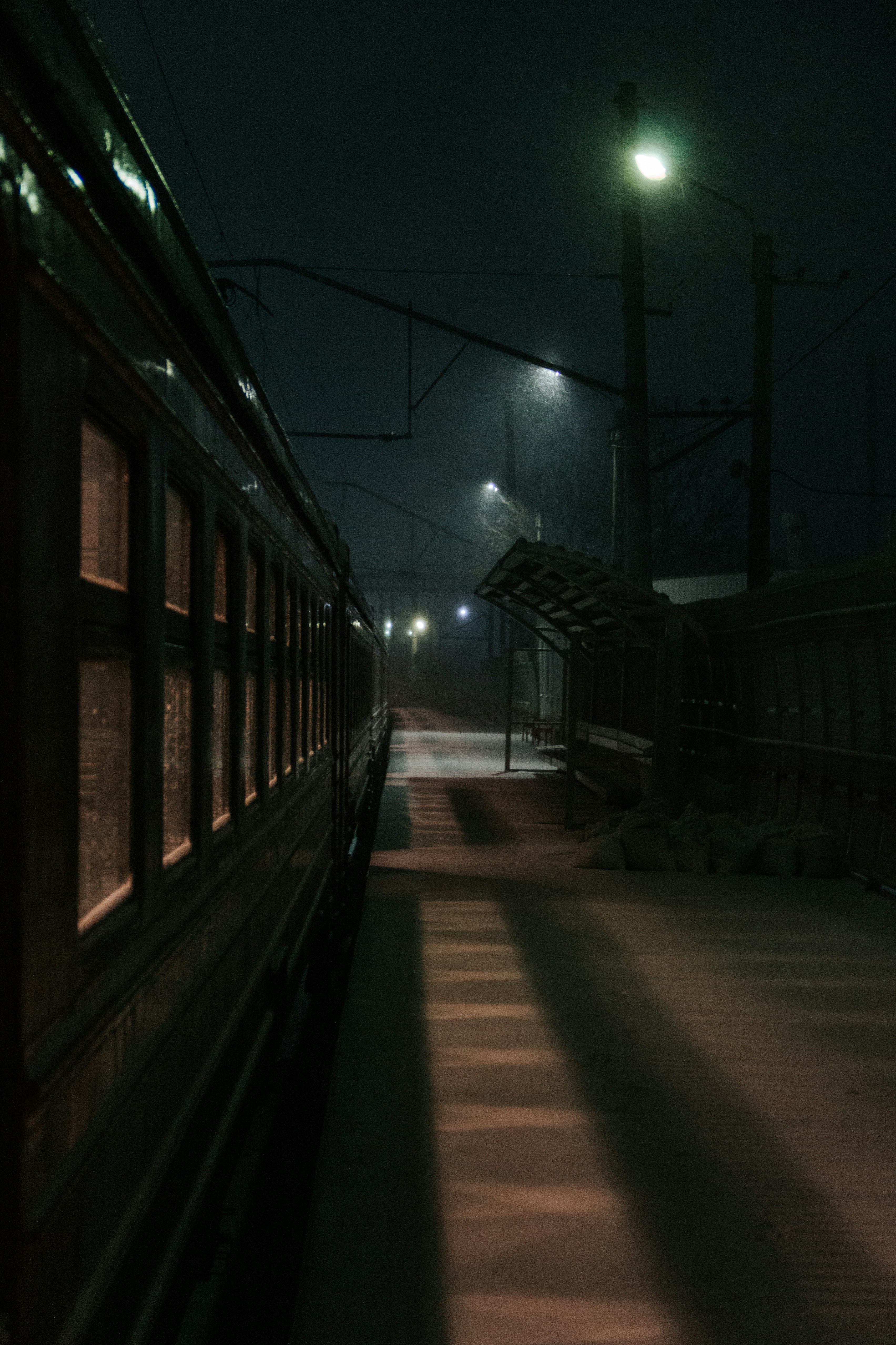 A train sits quietly at a dimly lit station, with snow gently falling and shadows stretching across the platform.