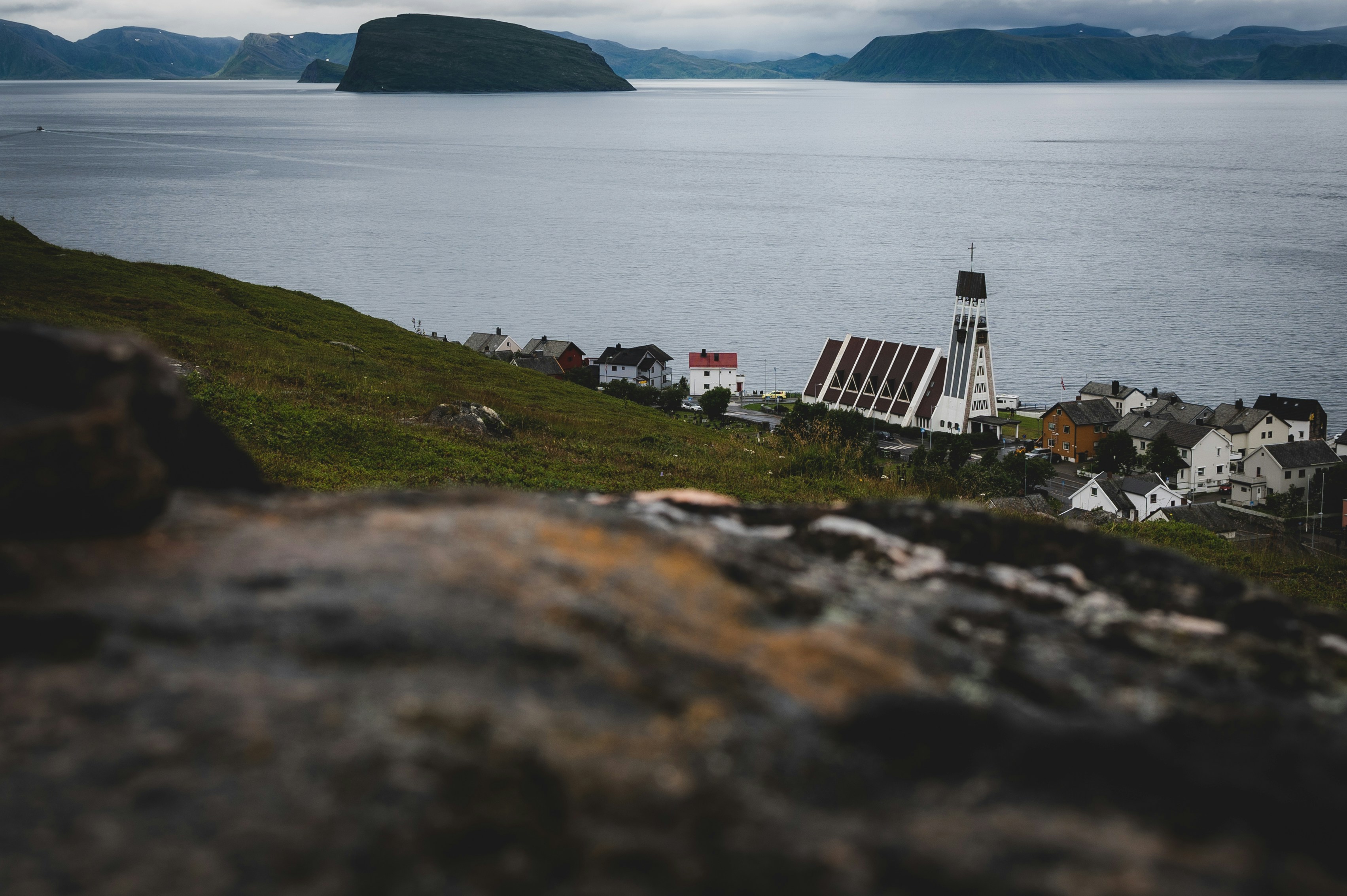 Distant view of a small coastal town with a prominent church and calm sea under a cloudy sky.