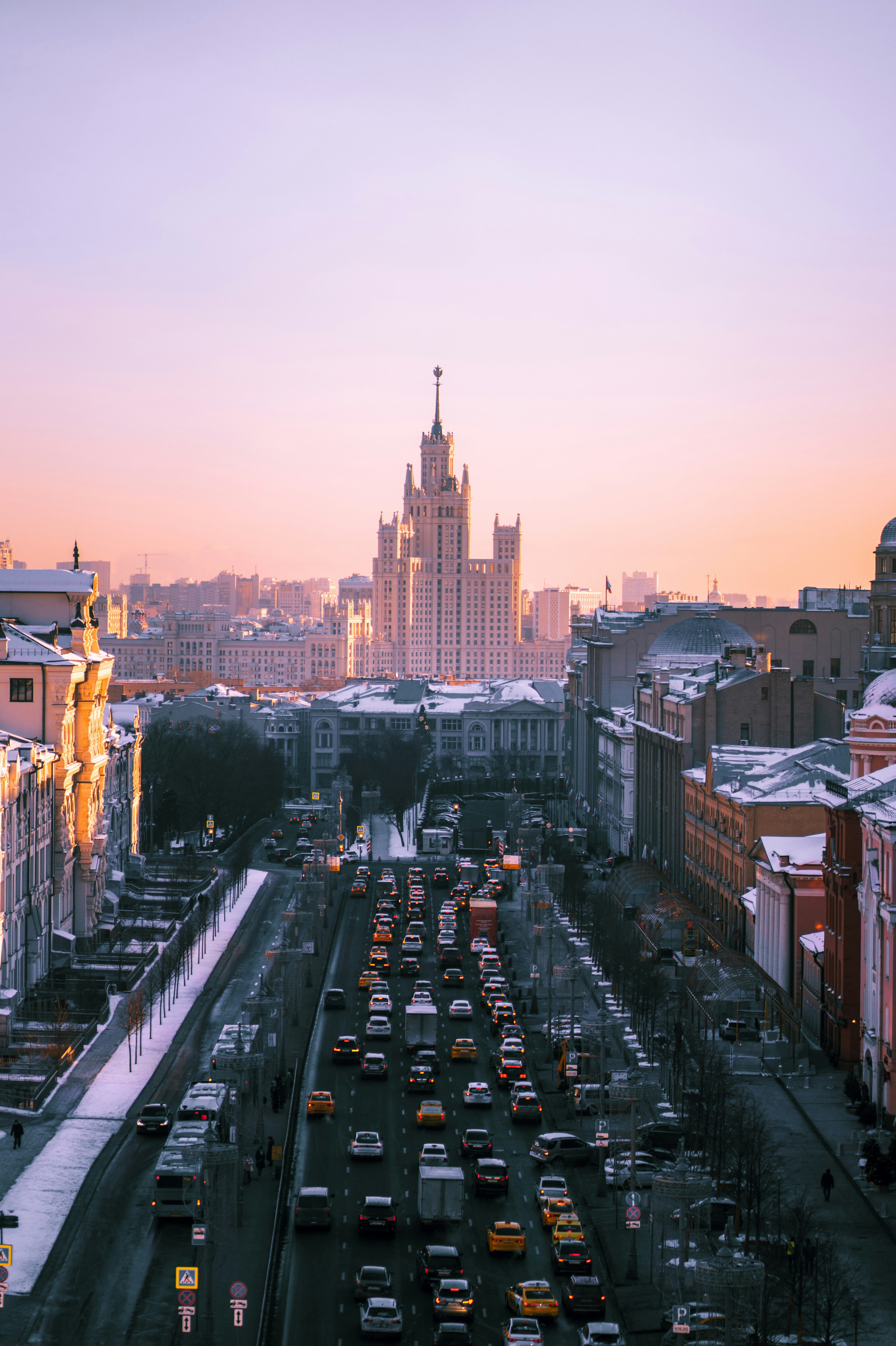 A bustling city street filled with traffic, framed by historic architecture and a prominent skyscraper in the background during twilight.
