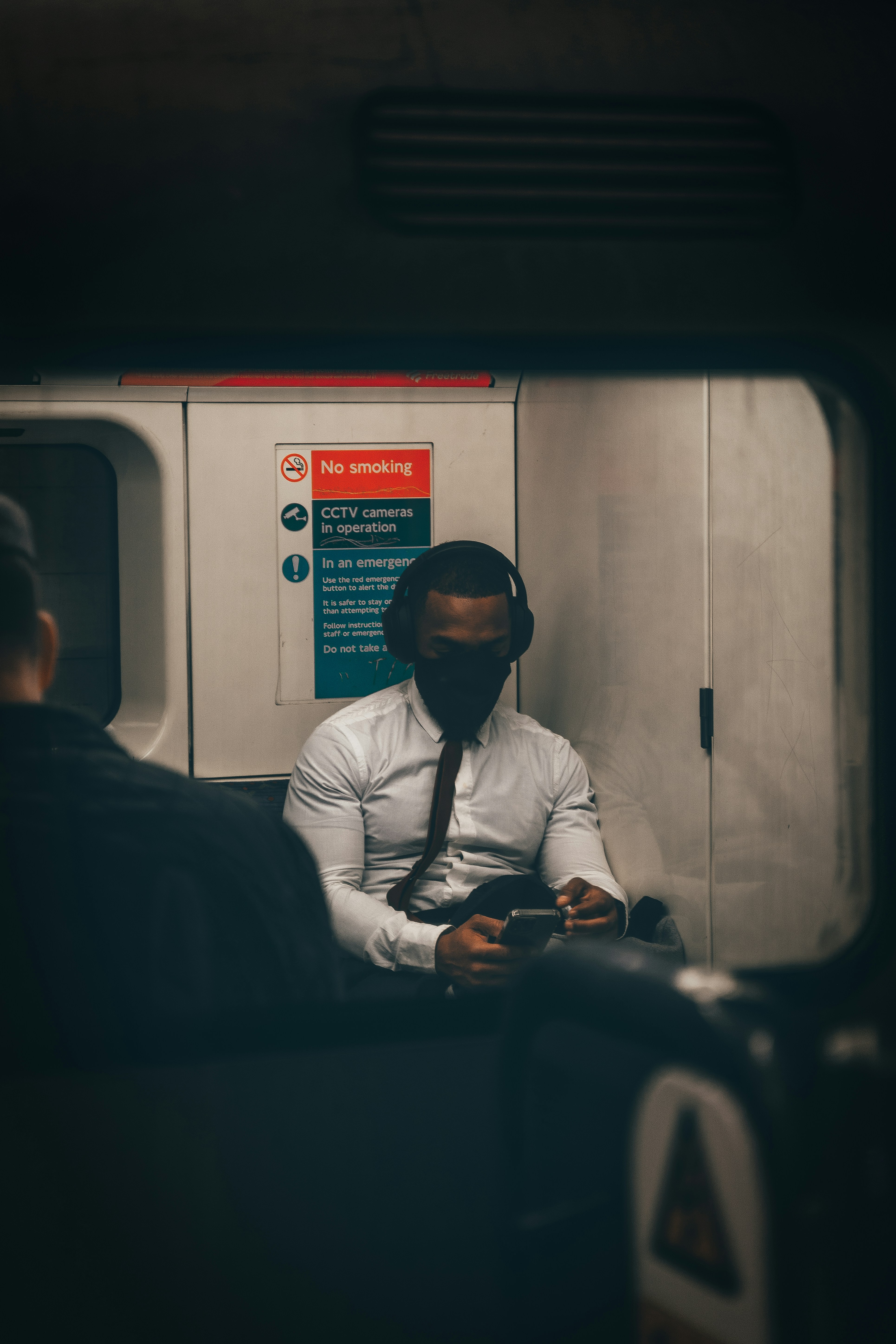 A man in a white shirt and tie, wearing headphones, absorbed in his phone while seated on a subway. The scene captures the essence of urban life and solitary moments in public transport.