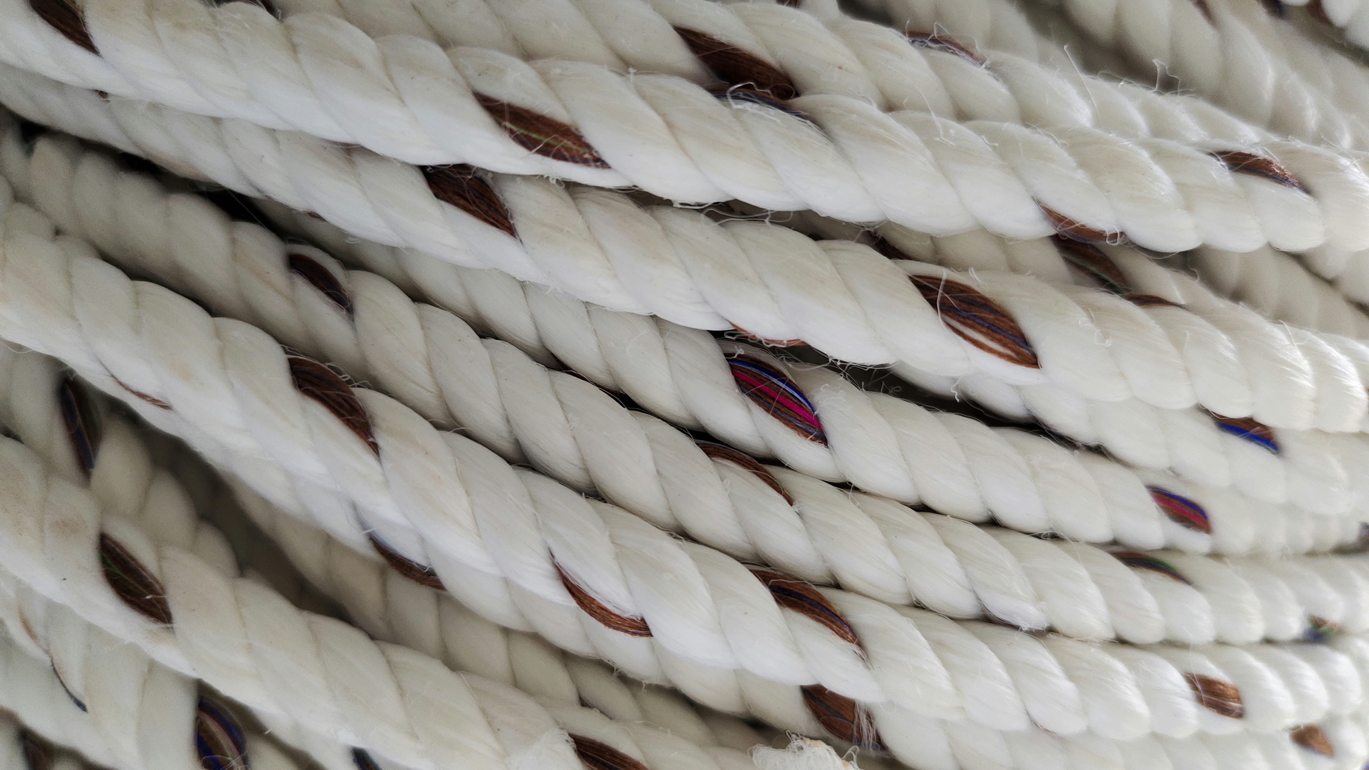 Macro photograph highlighting tightly wound white rope with faint purple fibers peeking through. It emphasizes the texture and weave pattern, drawing attention to material detail.