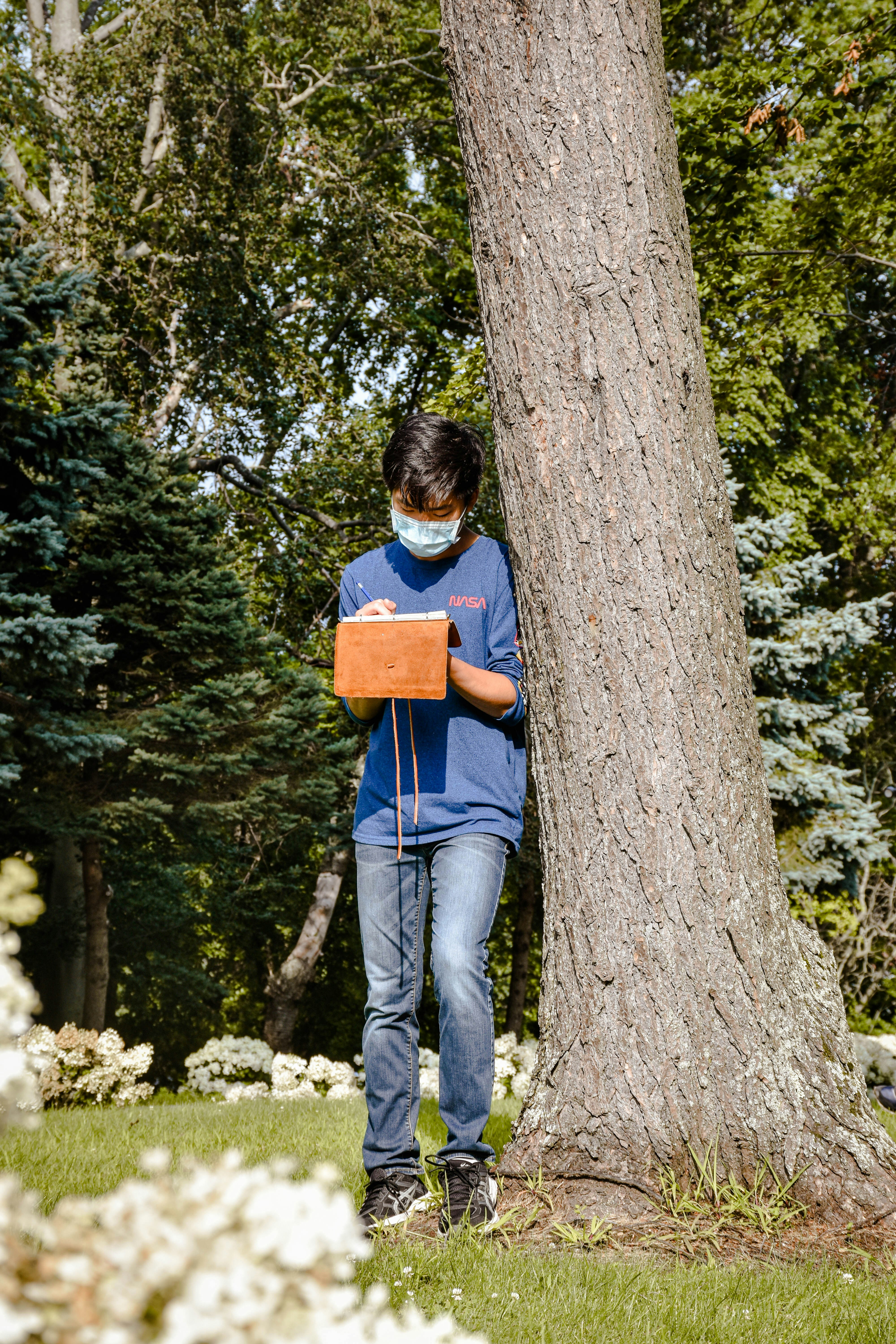 Masked student documenting nature by a towering tree