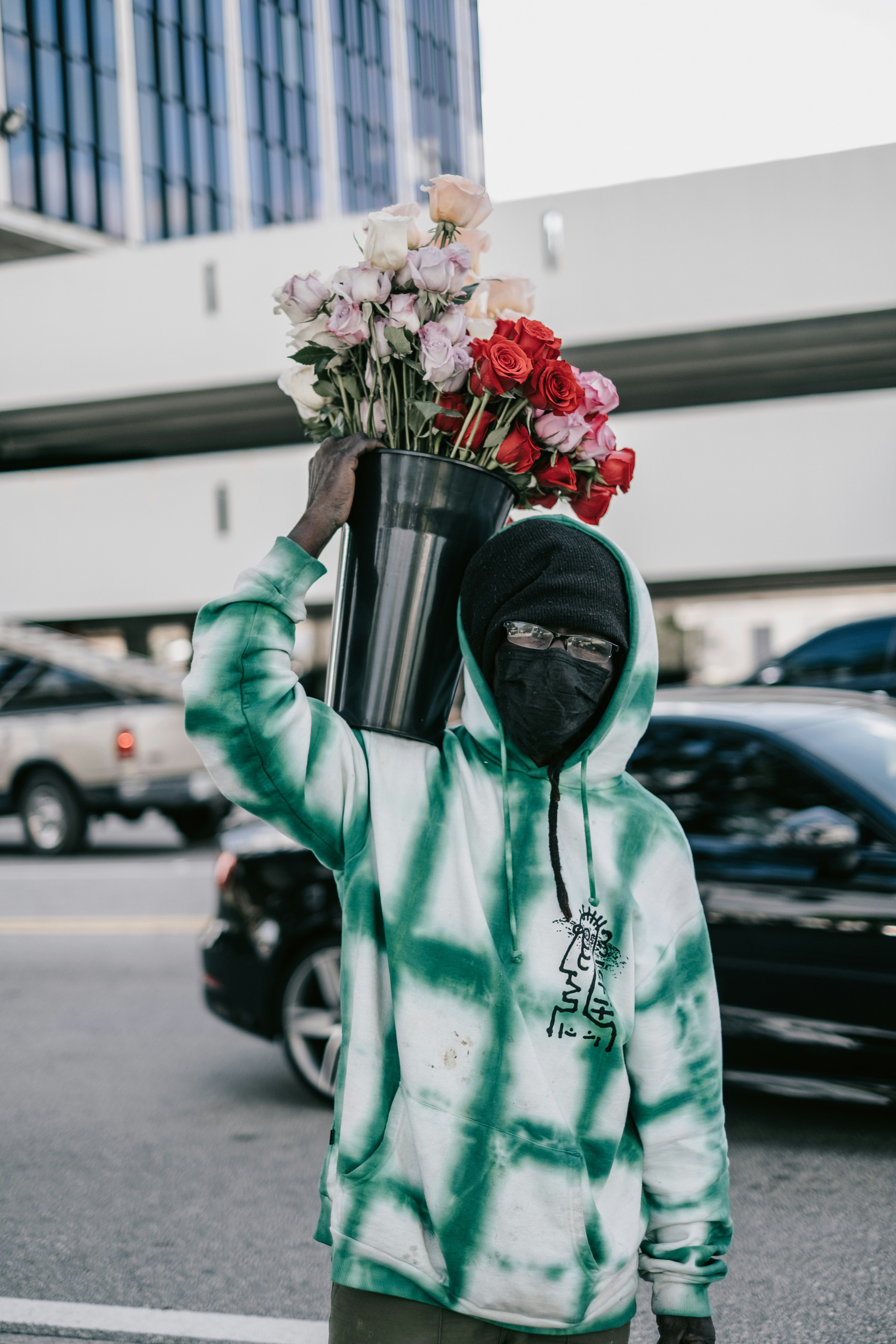 Bouquet atop a Hood: A Street Performer’s Bold Pose in Green Tie-Dye