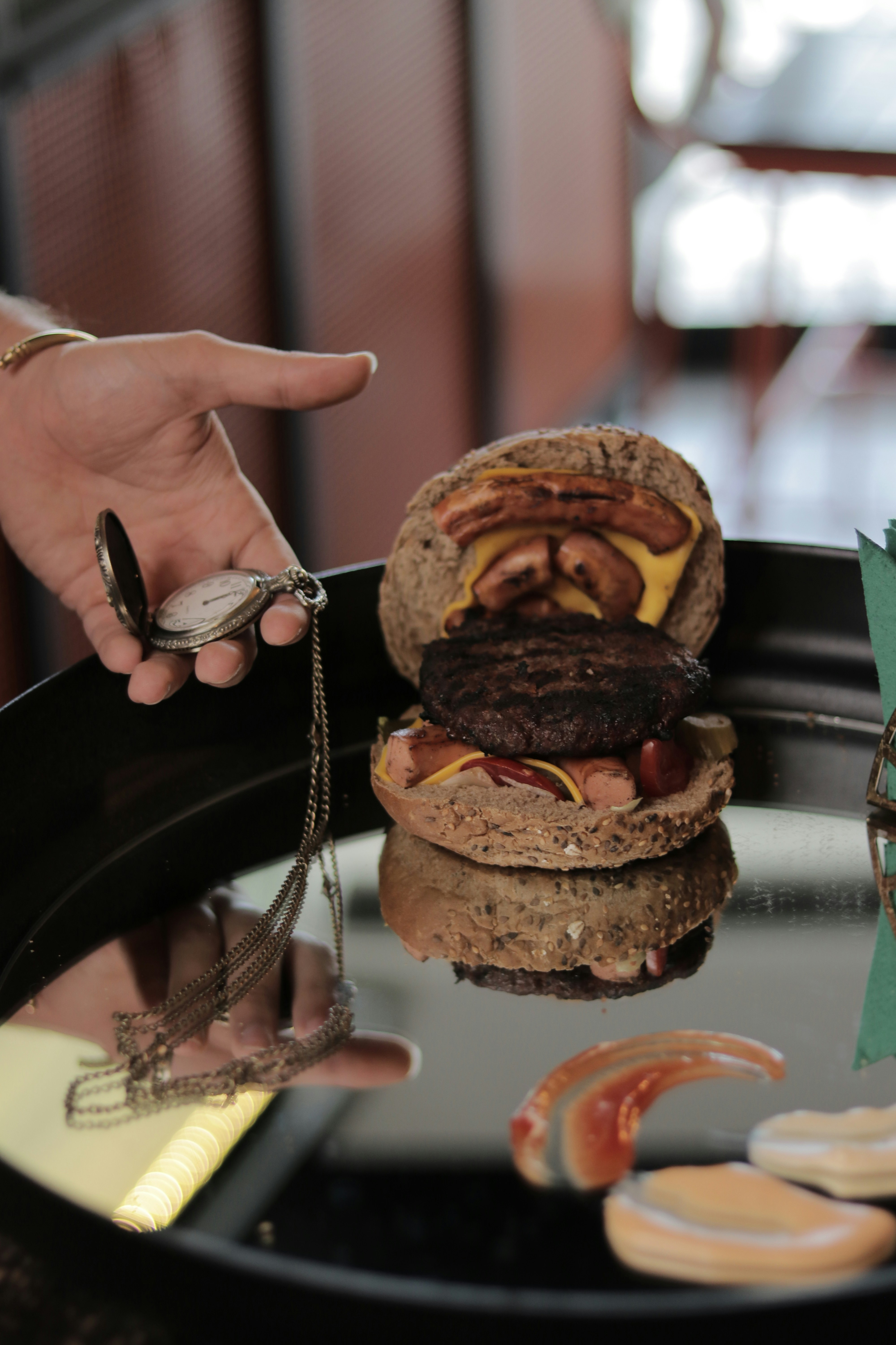 A gourmet burger featuring a unique combination of toppings, presented on a reflective surface, with a pocket watch in hand, symbolizing the intersection of time and taste.