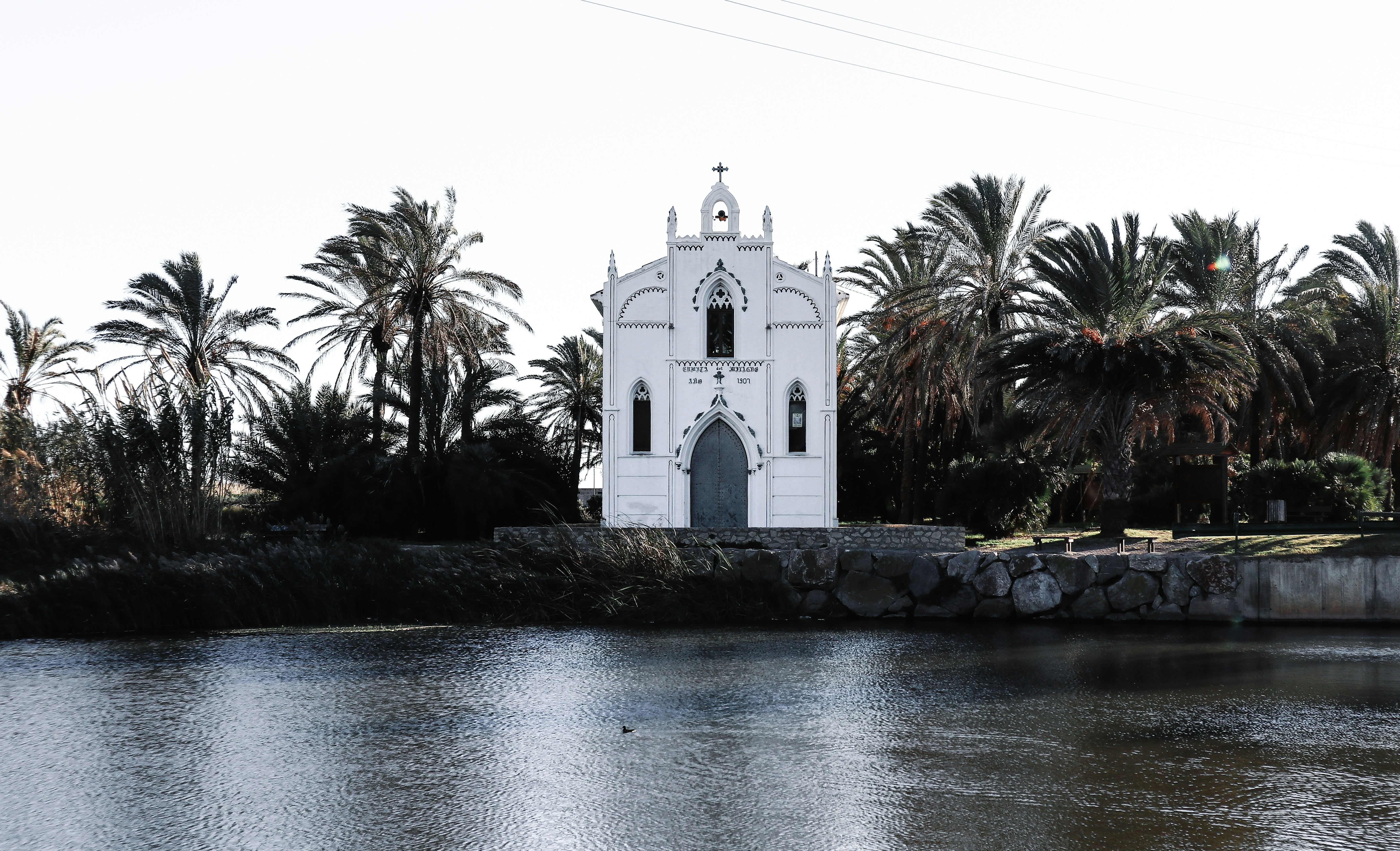 Arched White Chapel Framed by Palms Along a Calm Riverside