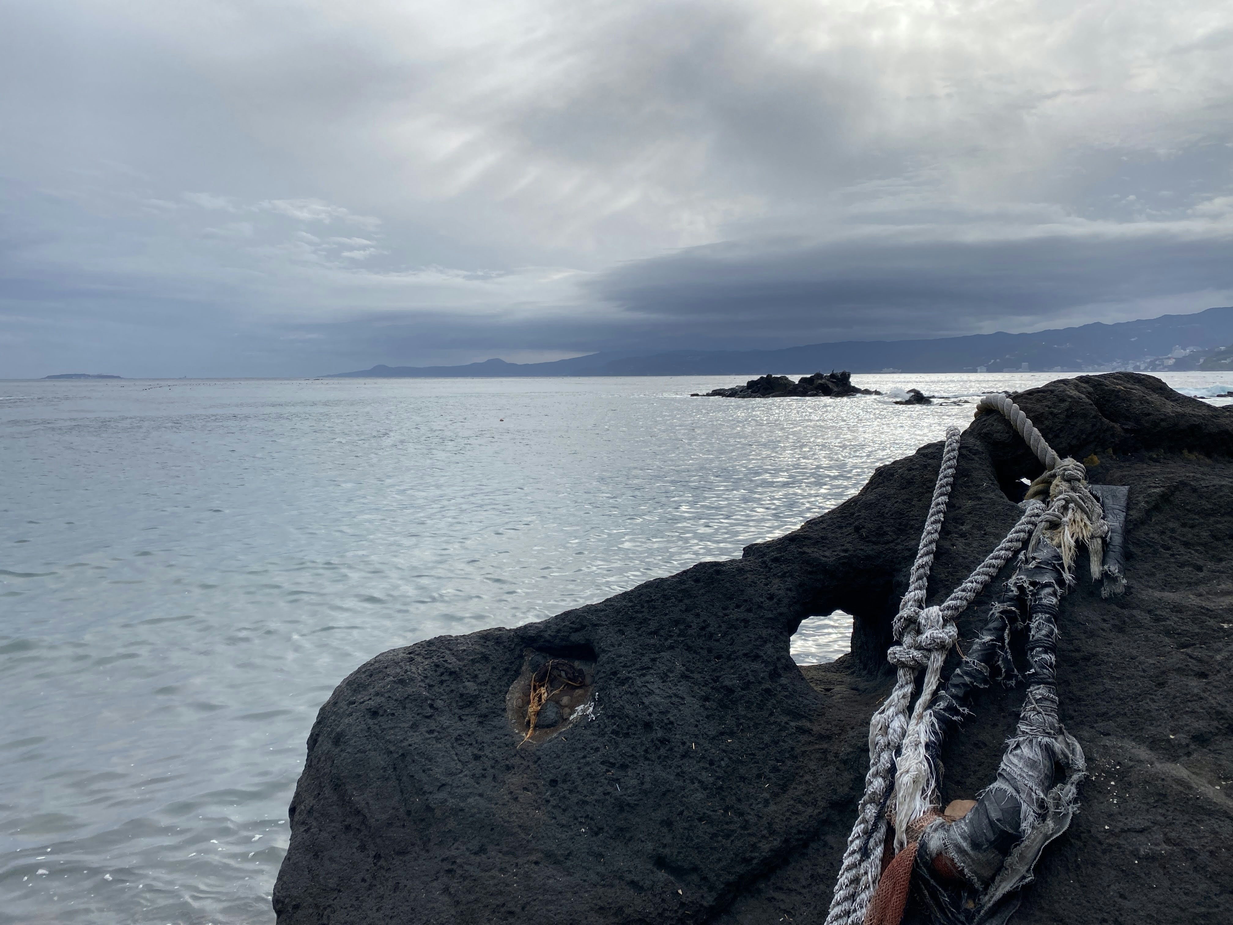 Rope draped over a rugged rock formation with a serene seascape in the background, hinting at nature's calmness before a storm.
