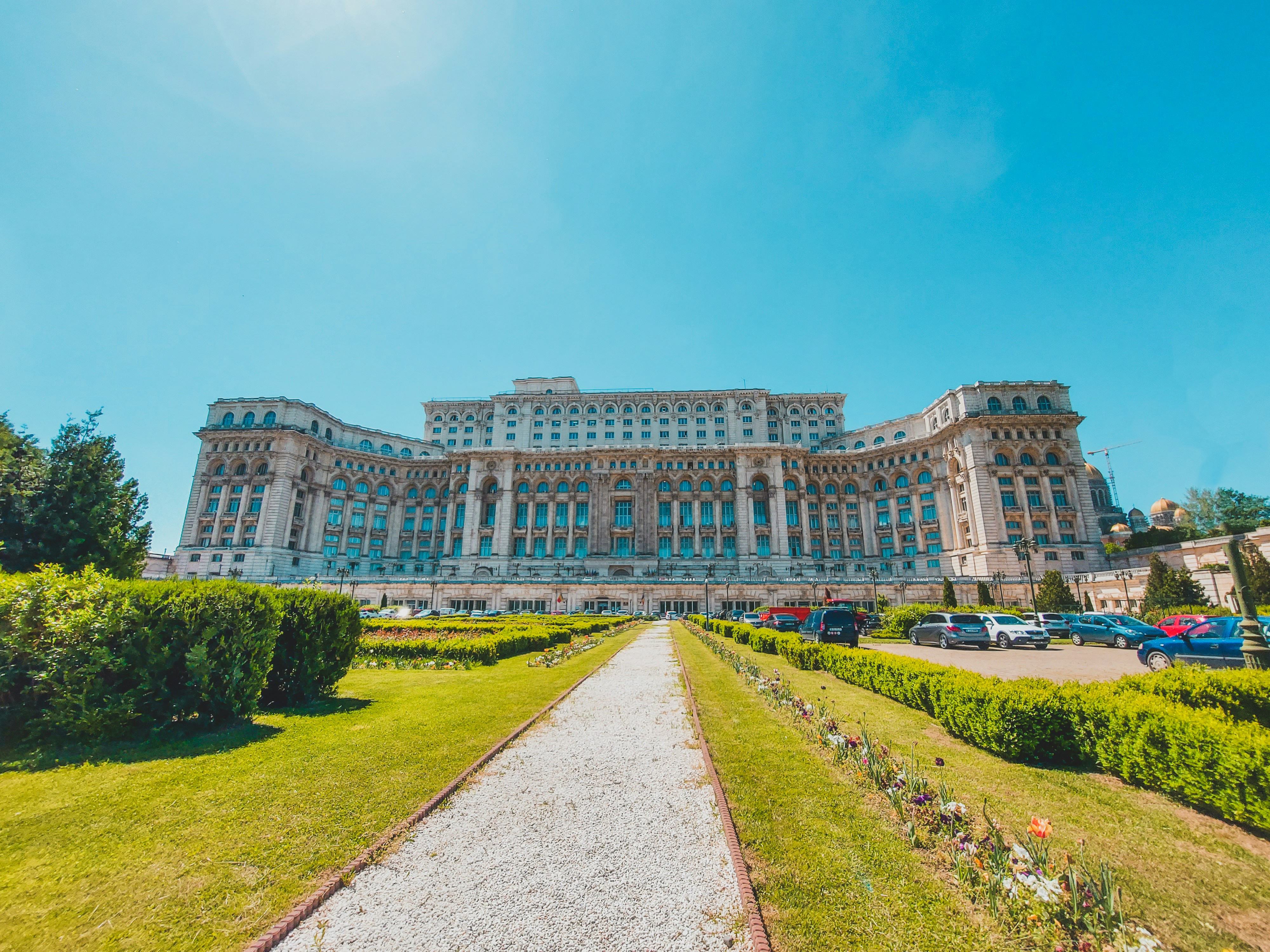 Expansive view of the Palace of Parliament under a clear blue sky, framed by manicured gardens.