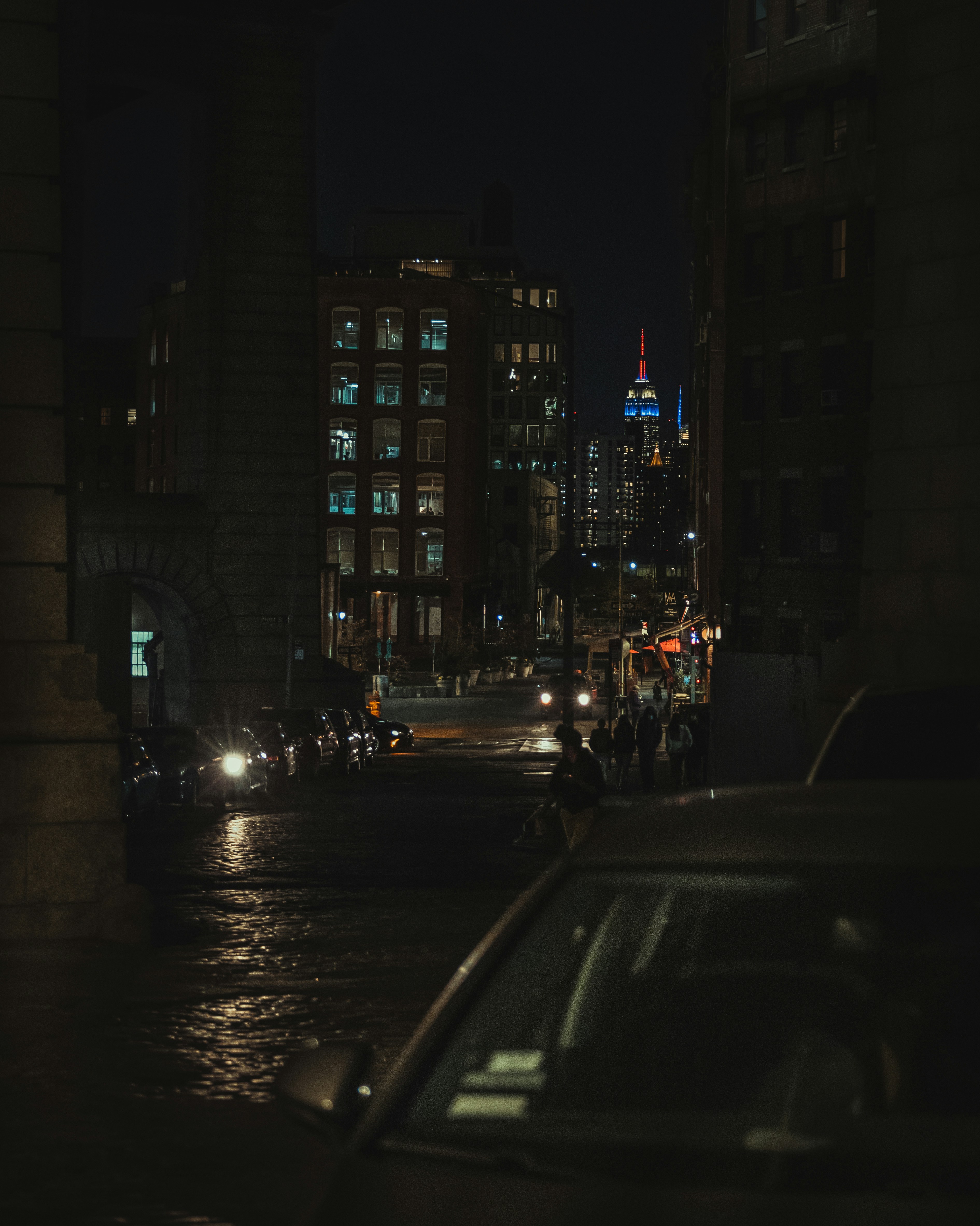 Blue Spire in the Night Corridor: A Street-Level View Toward the Distant Skyline