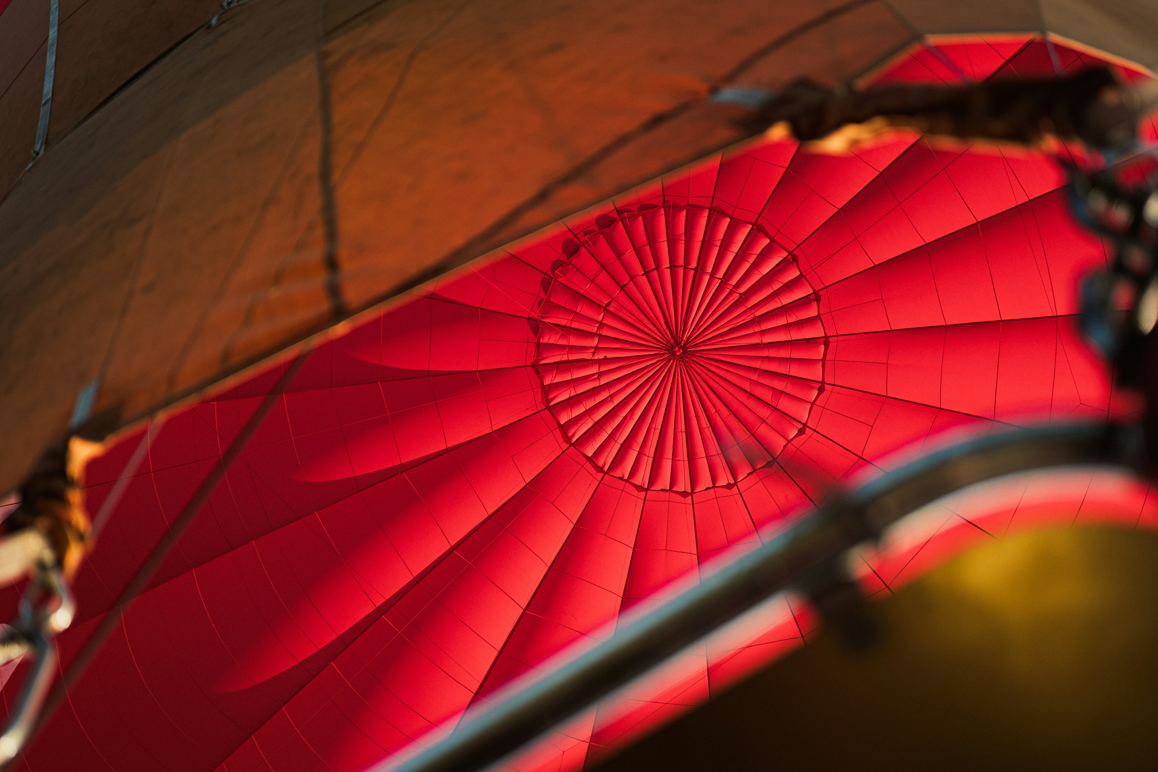Interior view of a hot air balloon showcasing the vibrant red fabric and intricate circular design. The image highlights the structure and texture of the balloon's canopy.