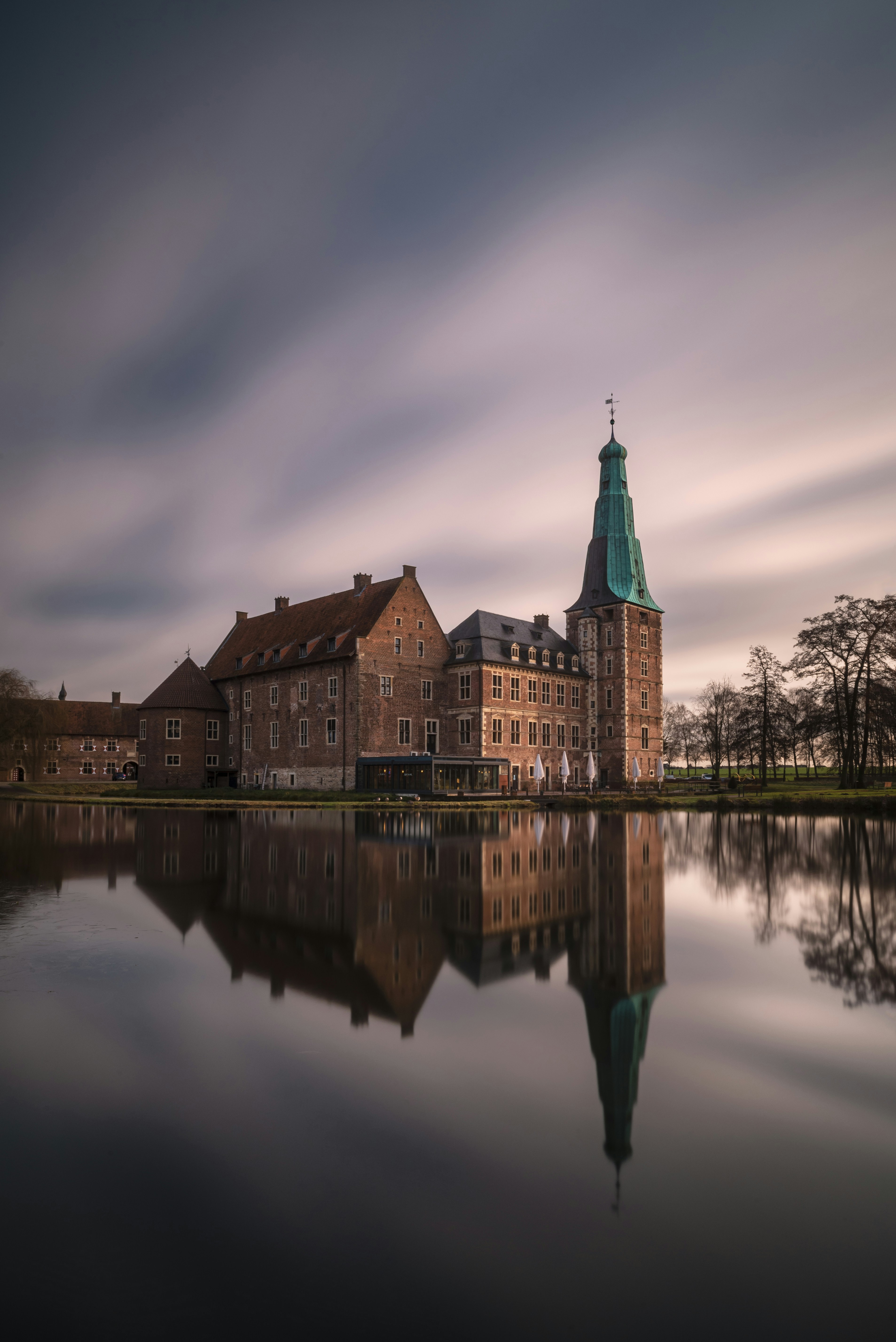Verdigris Spire Over a Riverside Castle Reflected in Glassy Water