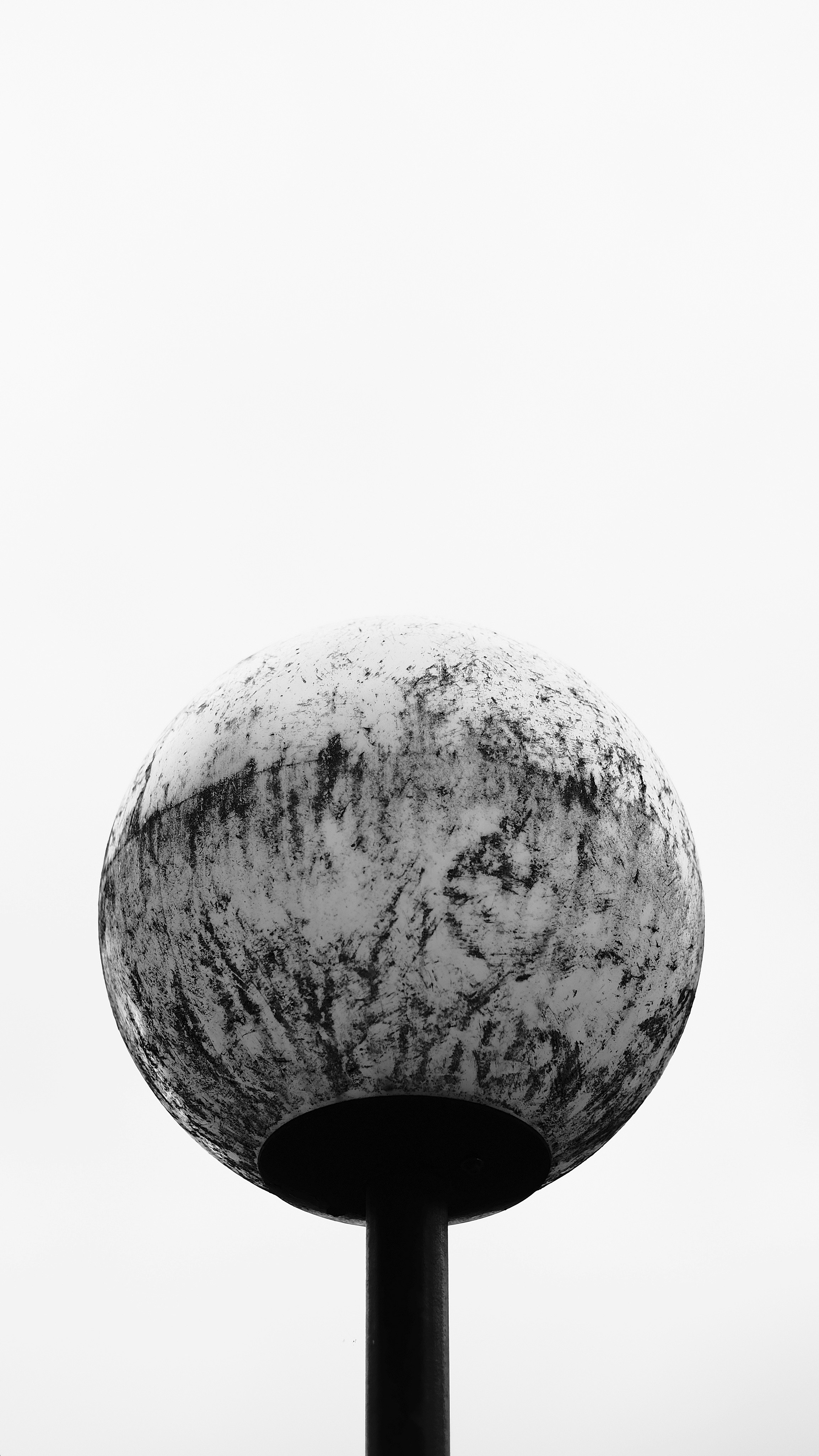 Weathered spherical light fixture against a stark white sky, highlighting its intricate surface details and minimalist aesthetic.
