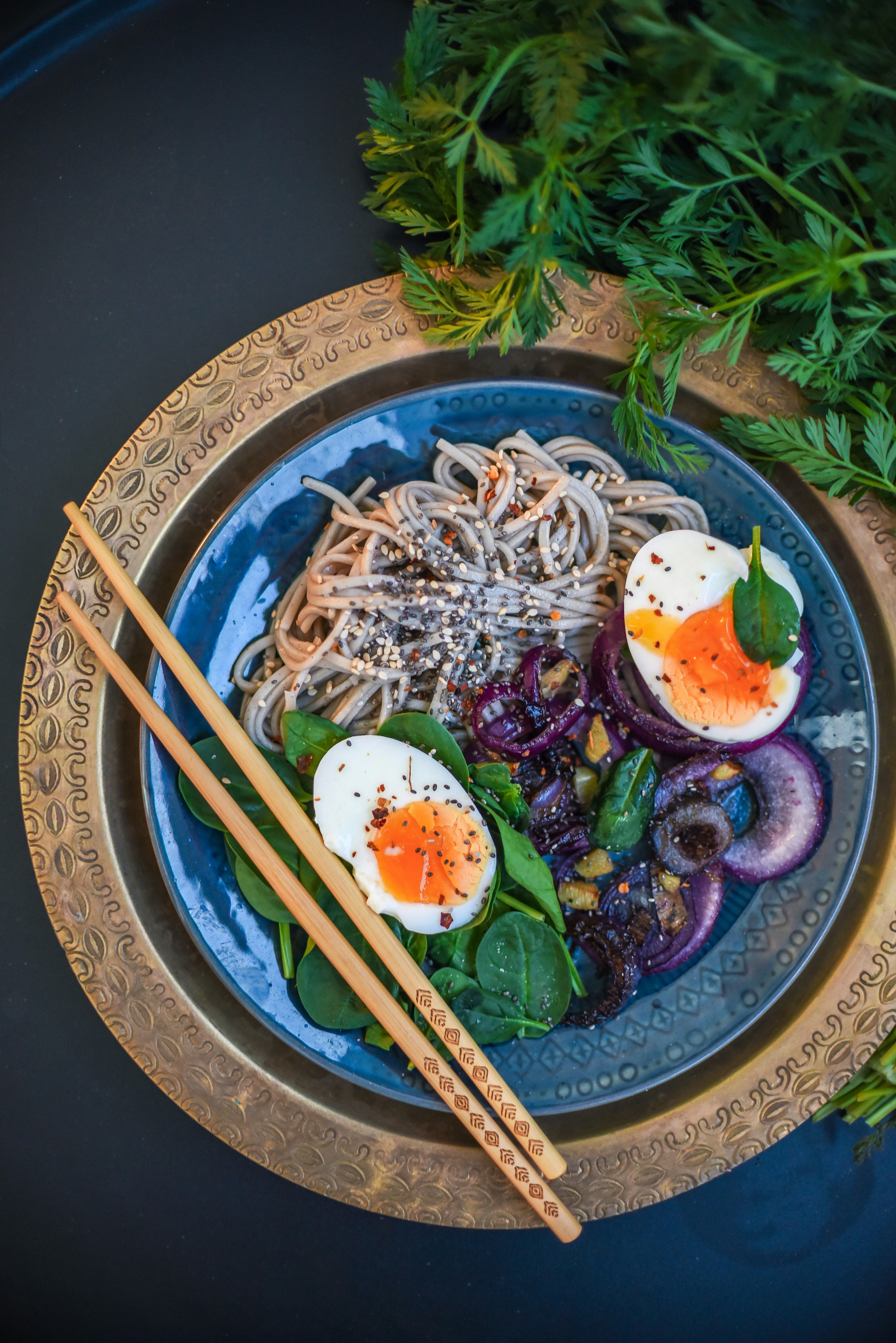 Artfully arranged soba noodles, vibrant vegetables, and soft-boiled eggs on an ornate plate, garnished with fresh greens.