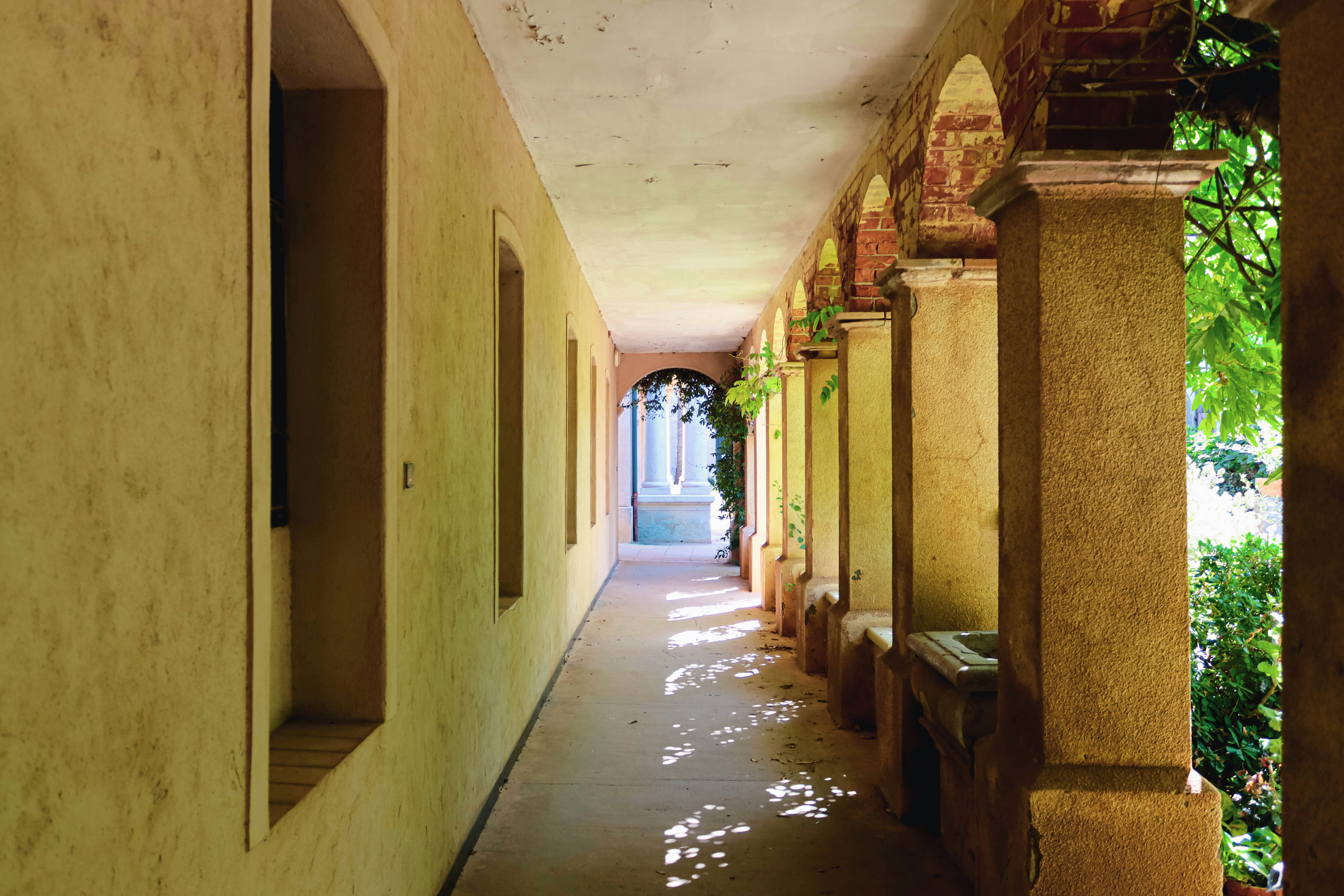 A long hallway with a bench between two buildings photo – Free Corridor ...