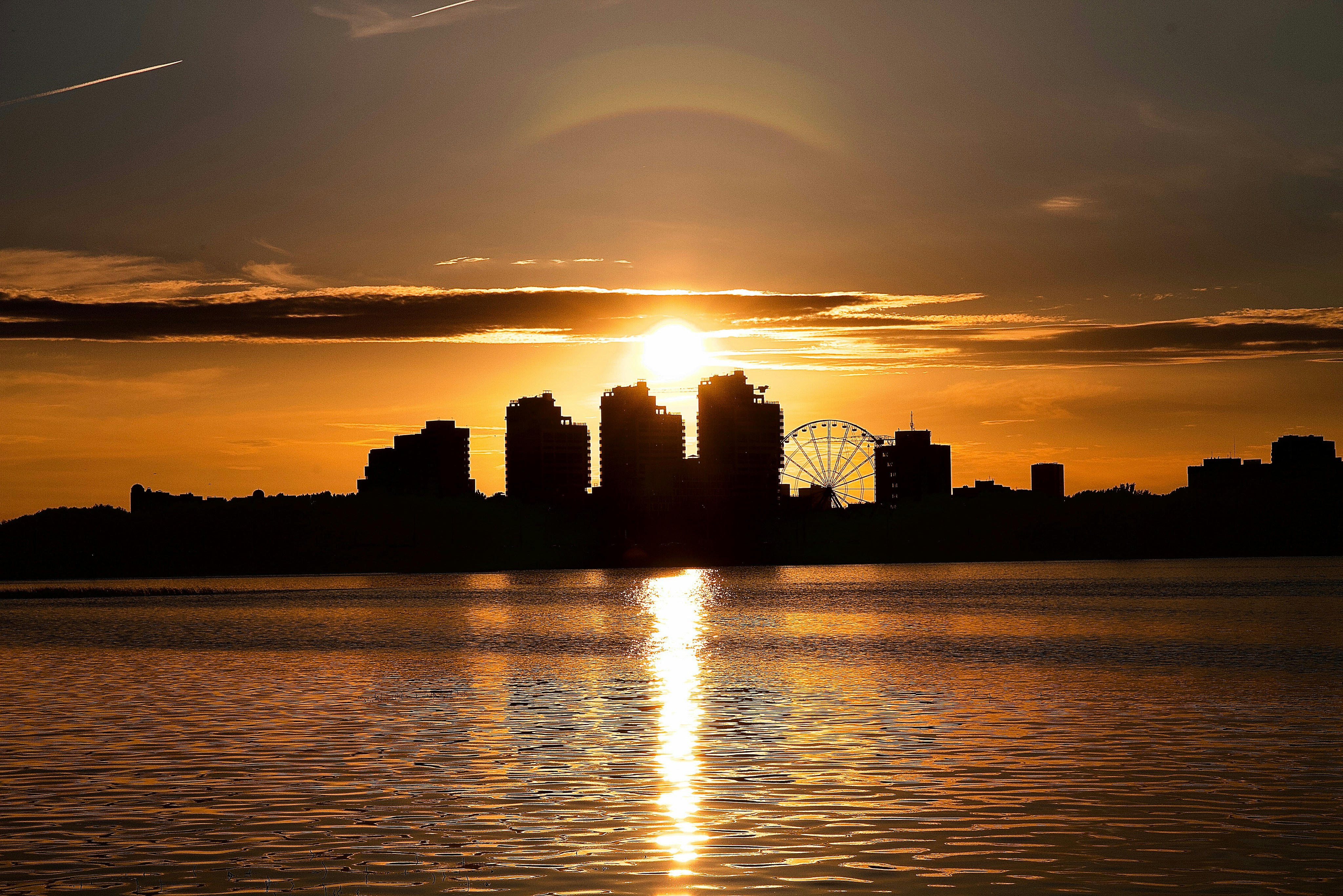 Silhouette of a city skyline against a vibrant sunset with reflections on calm water.