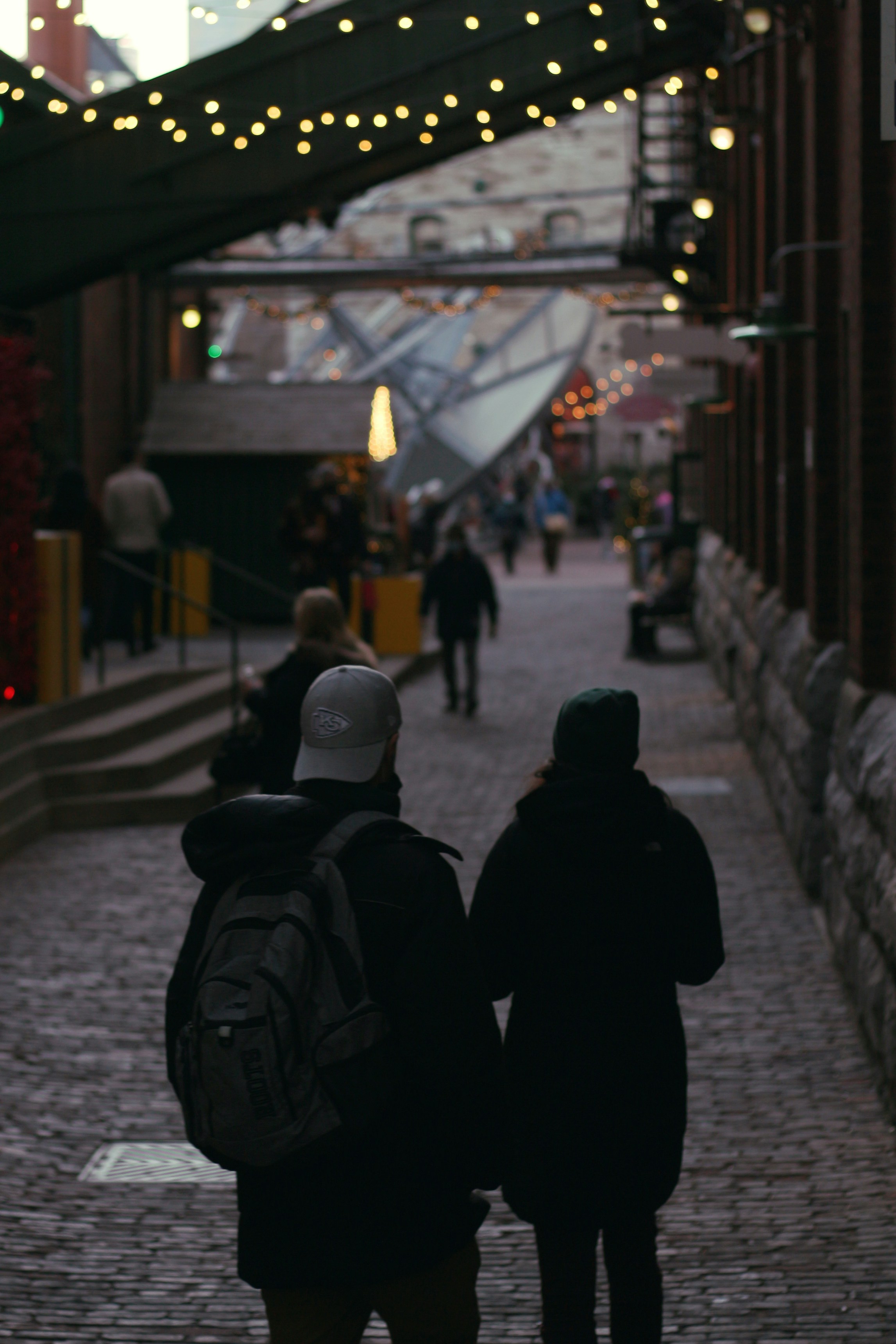 Silhouettes in a Cobblestoned Alley Beneath Festive String Lights