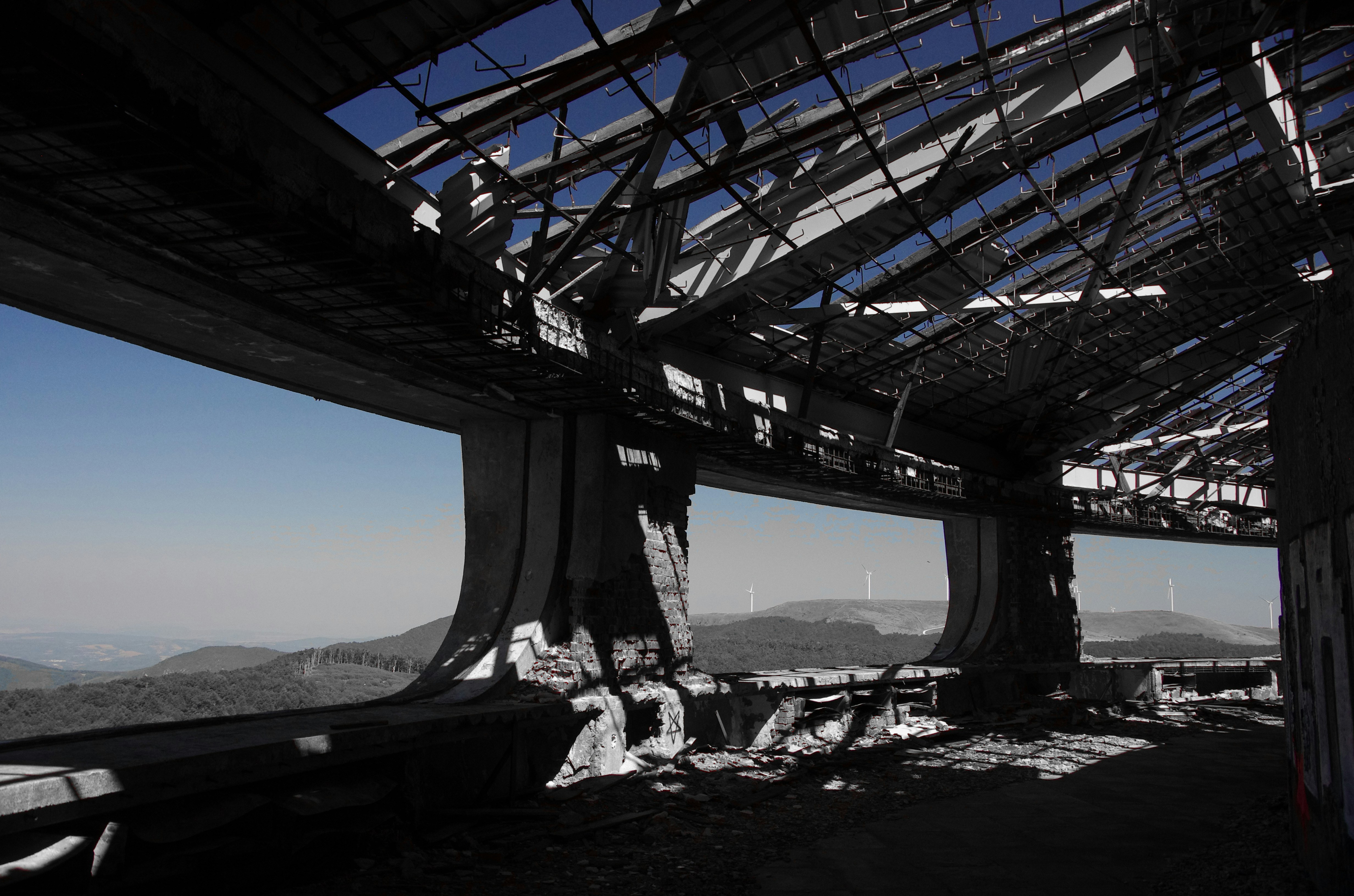 Photograph of a ruined industrial interior with skeletal arches and rubble, with a bright blue horizon visible through the openings.