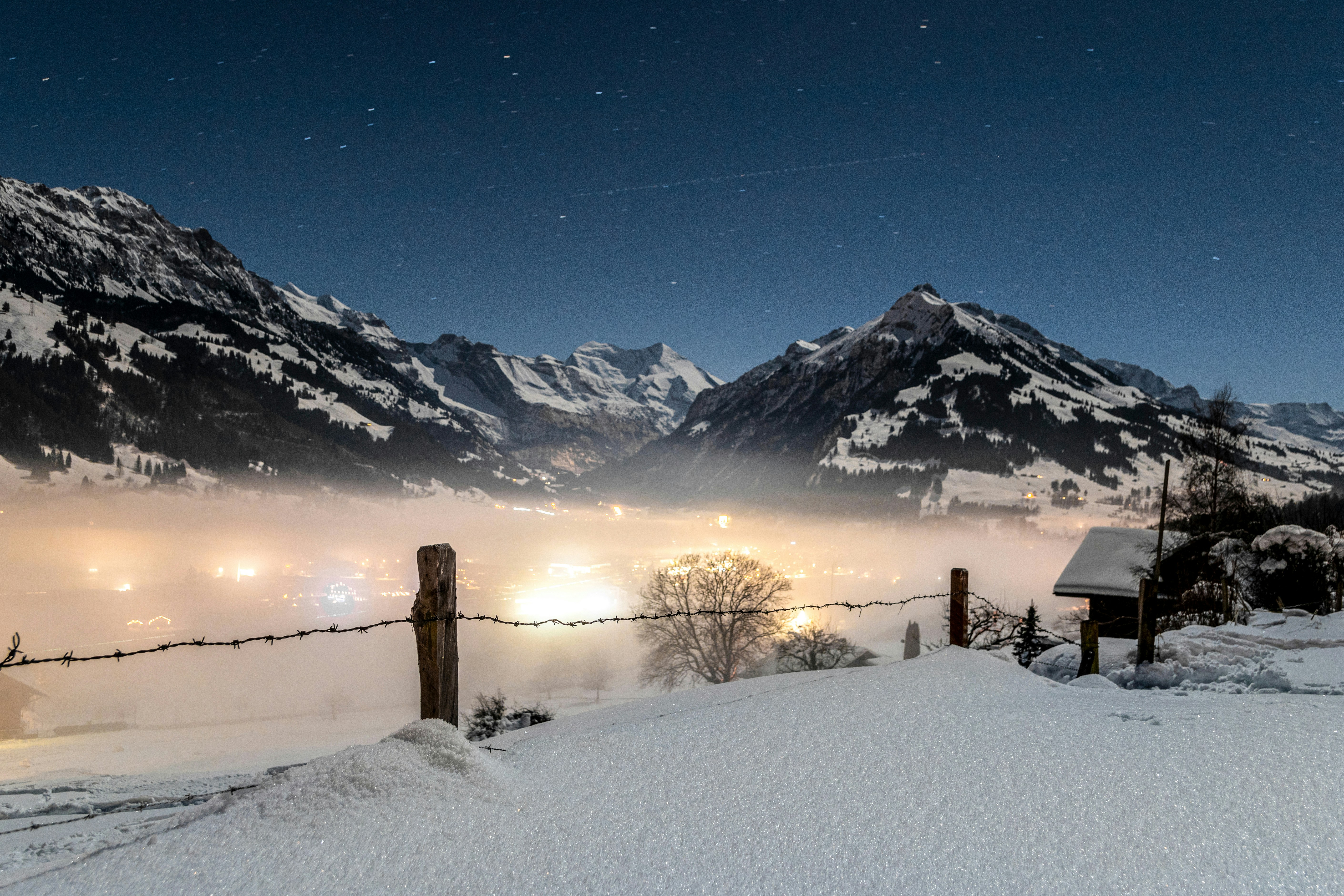 a snowy landscape with a fence and mountains in the background