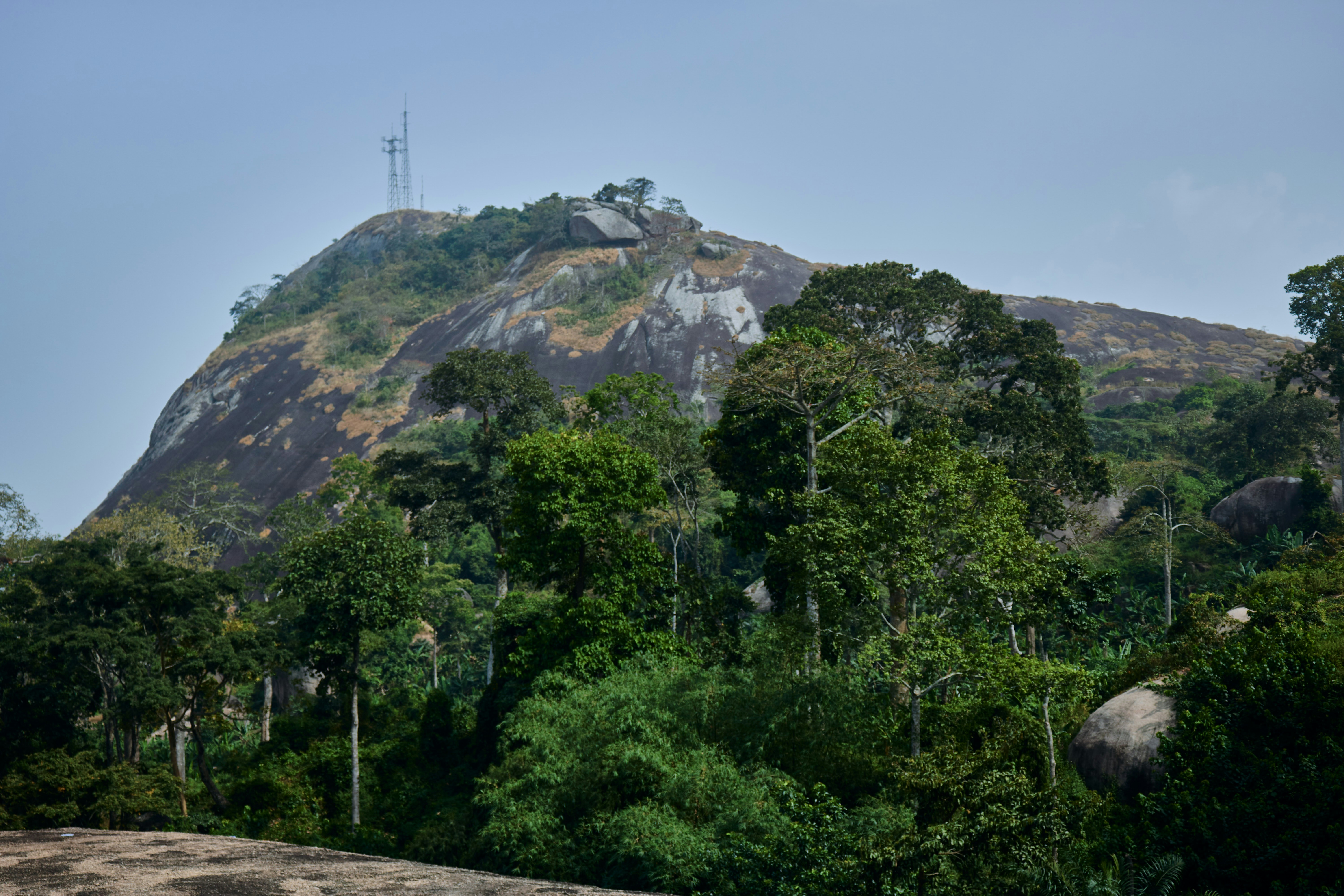 Lush green forest ascending a rocky hill with a communication tower at the summit.