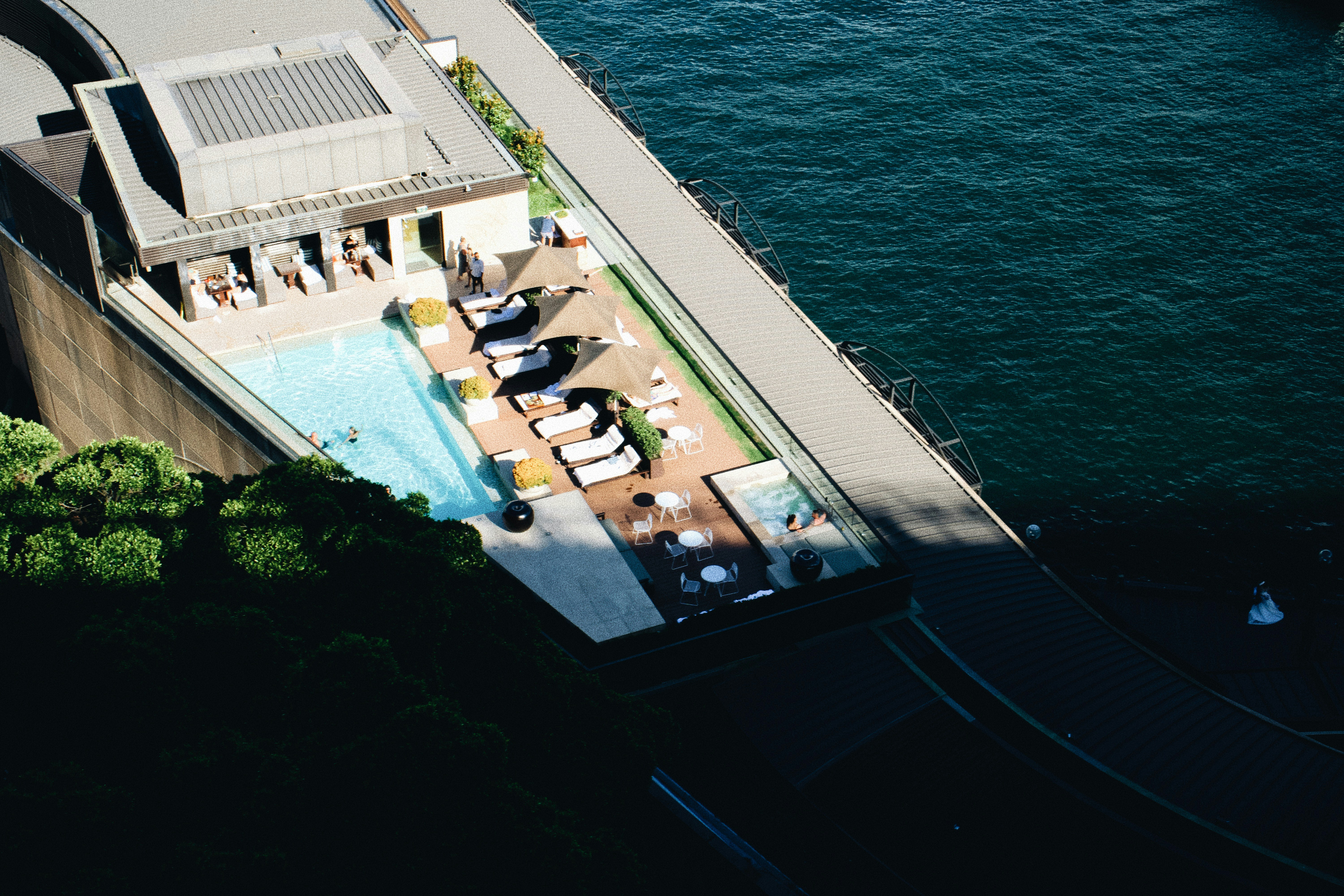 Stylish rooftop pool area featuring lounge chairs and umbrellas, overlooking a shimmering body of water. The scene captures the essence of relaxation in an urban setting.