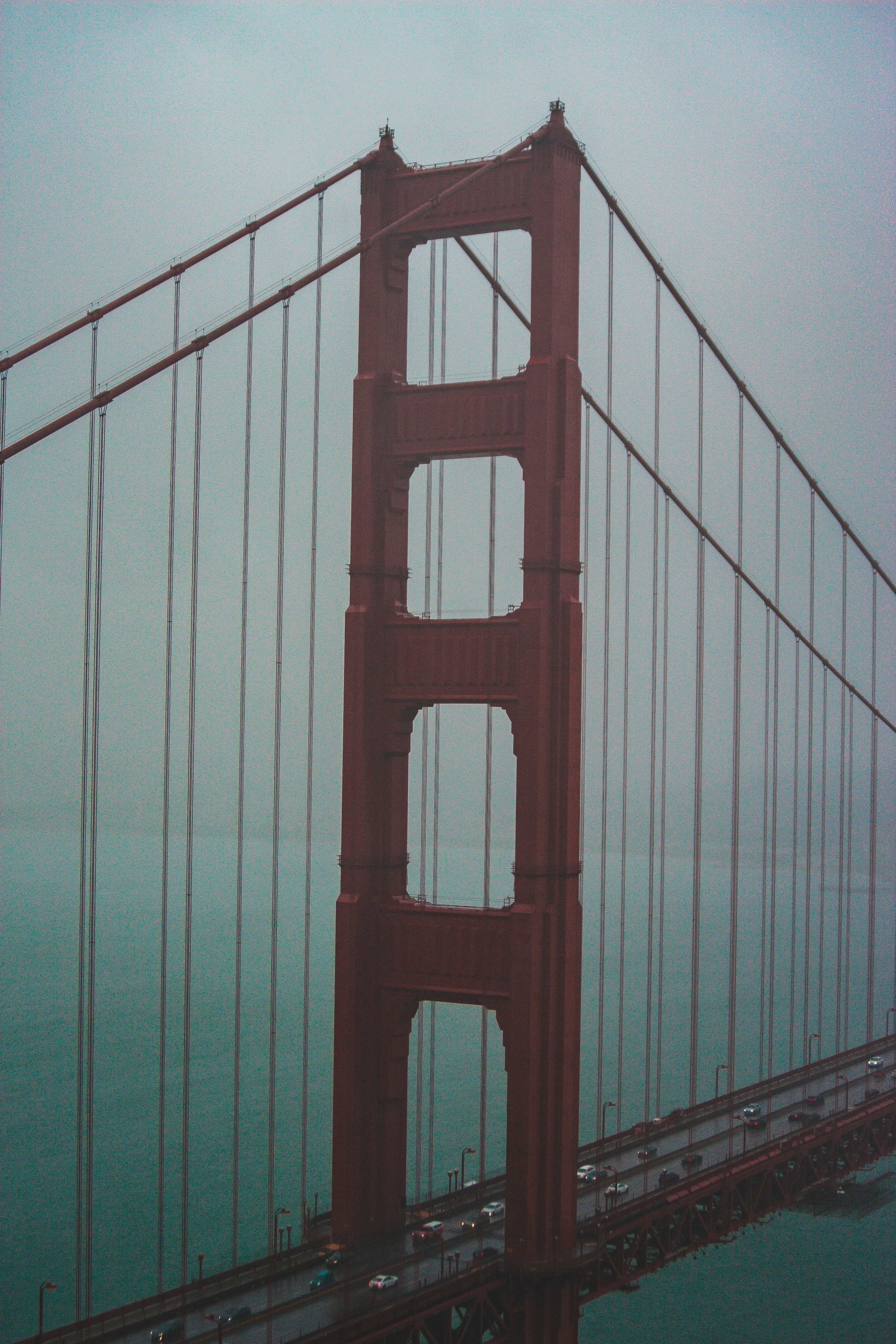 The Golden Gate Bridge emerges through a veil of fog, showcasing its iconic towers against a moody backdrop. The scene captures the bridge's architectural grandeur and the serene waters below.