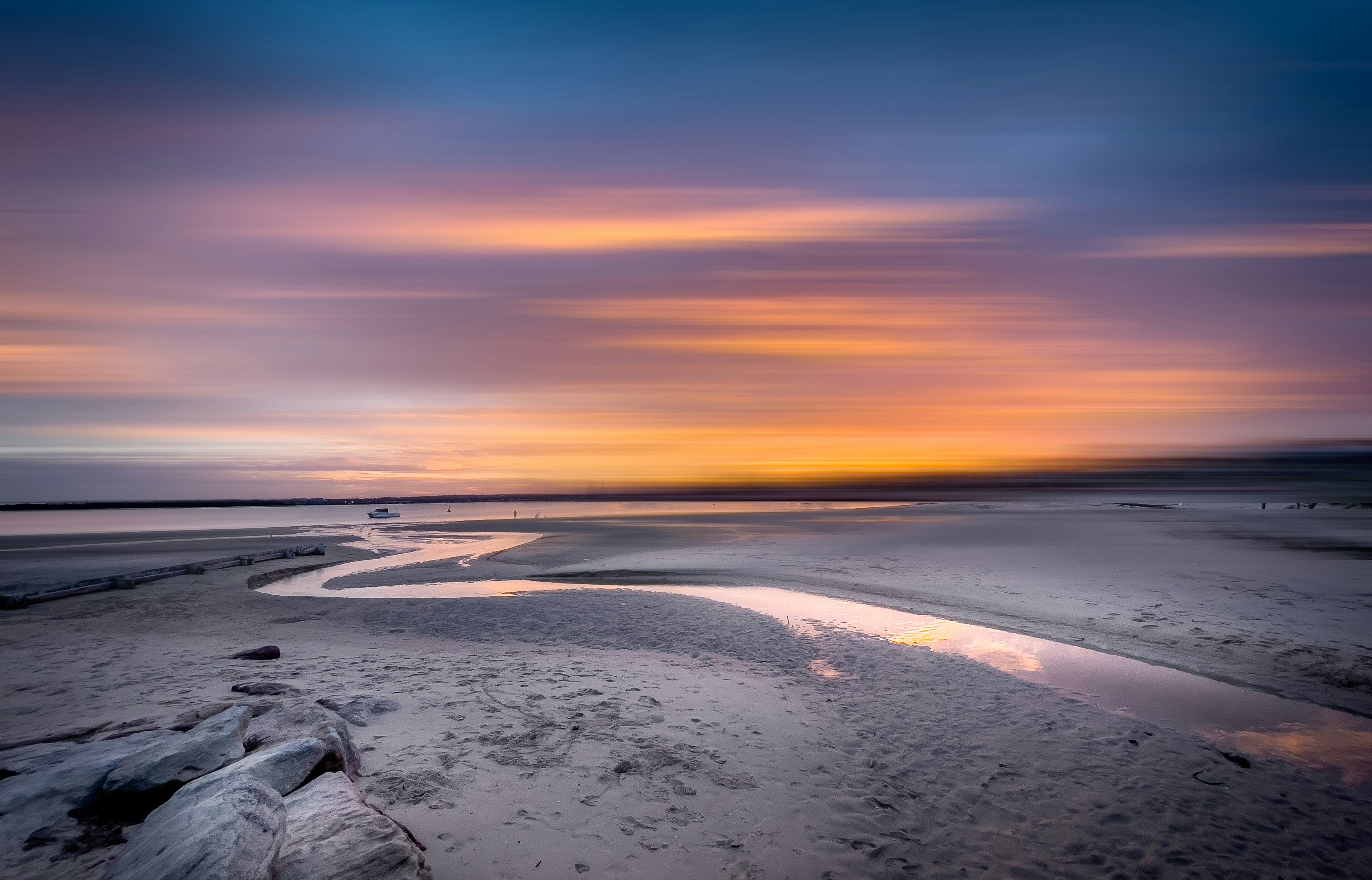 Gentle curves of a sandy shore lead to a tranquil estuary reflecting vibrant twilight hues.