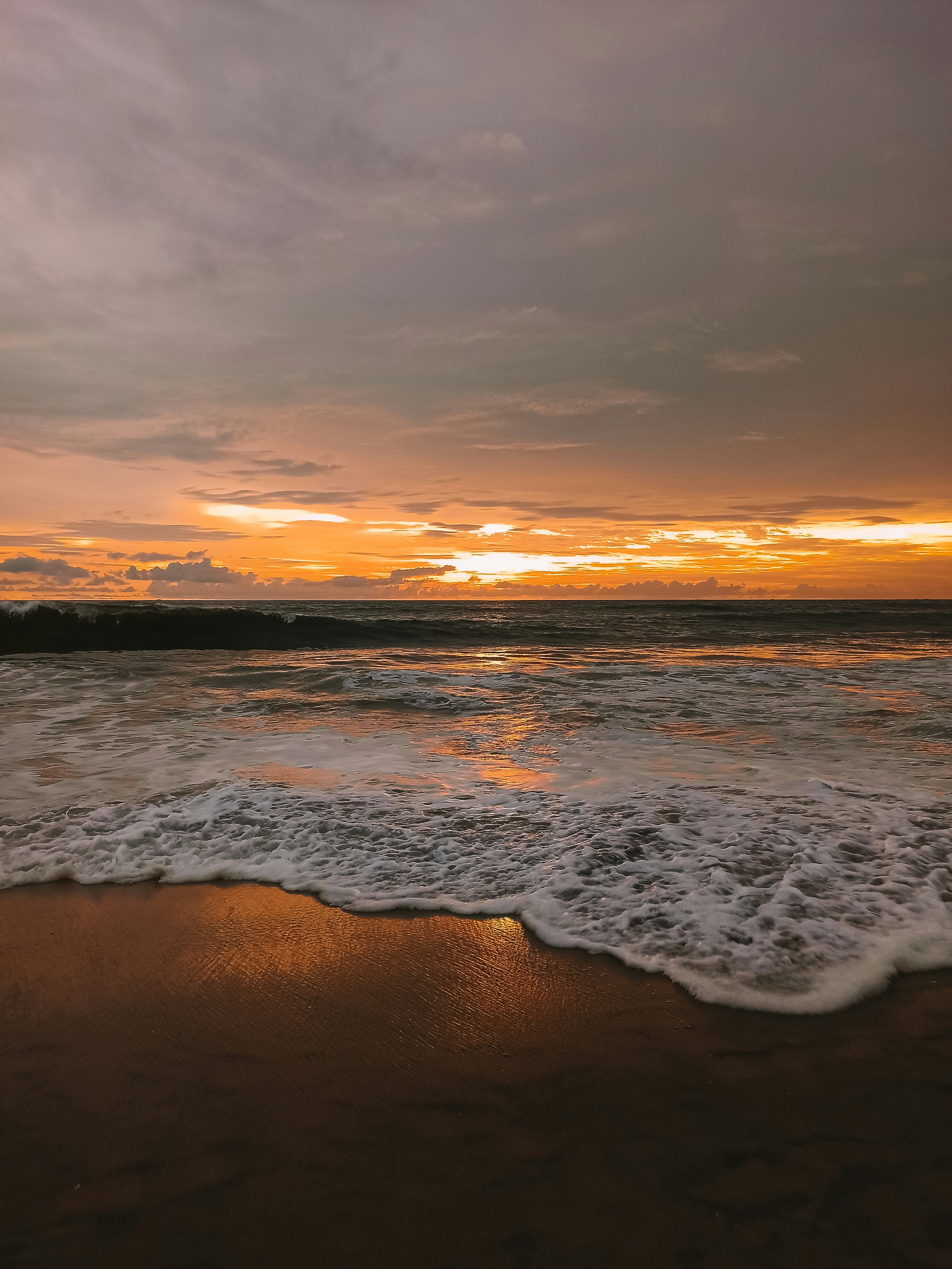 Gentle waves lapping at the shore under a dramatic sunset sky, showcasing vibrant hues of orange and purple.