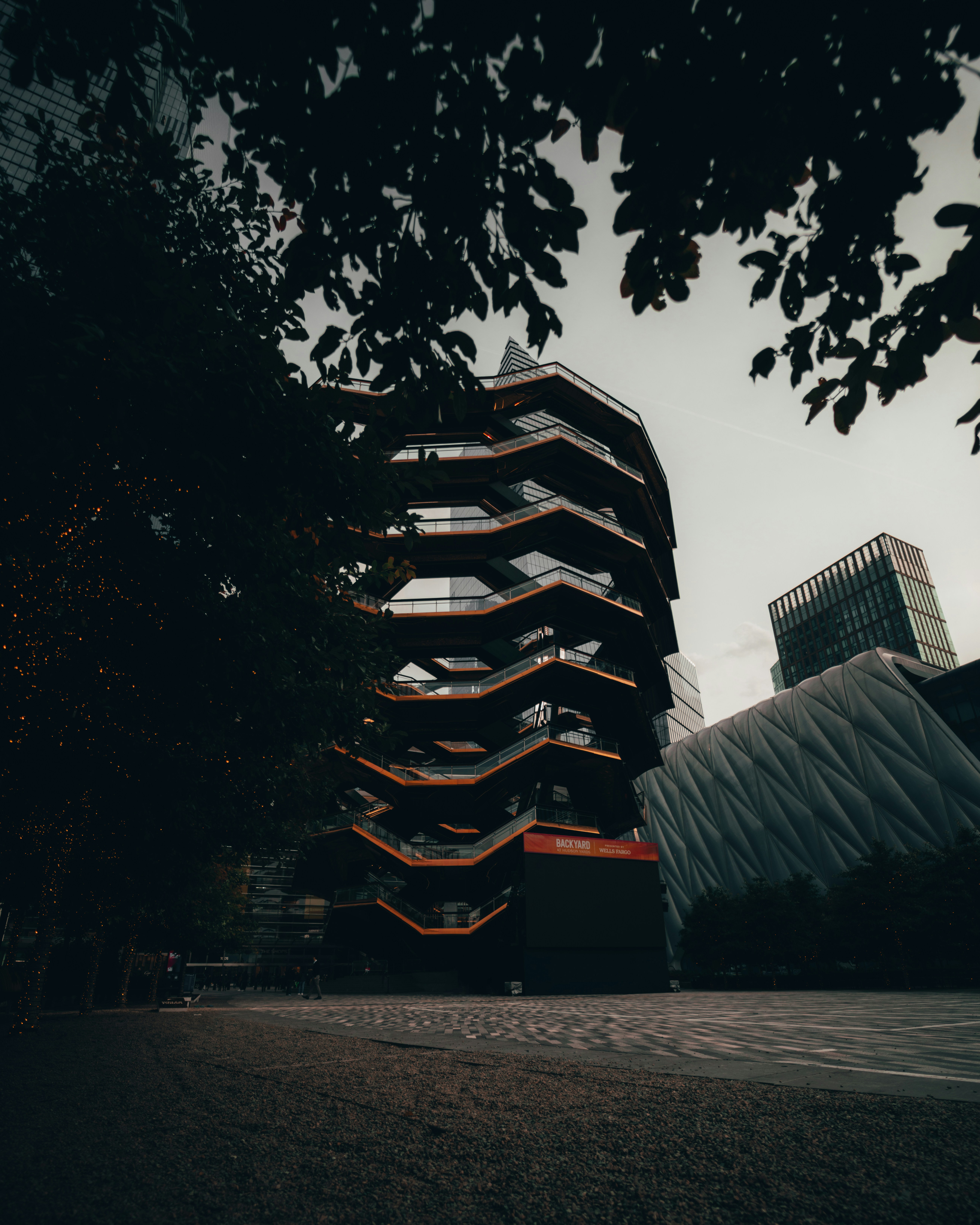Stacked Balconies at Dusk: An Urban Tower Framed by Shadowed Foliage