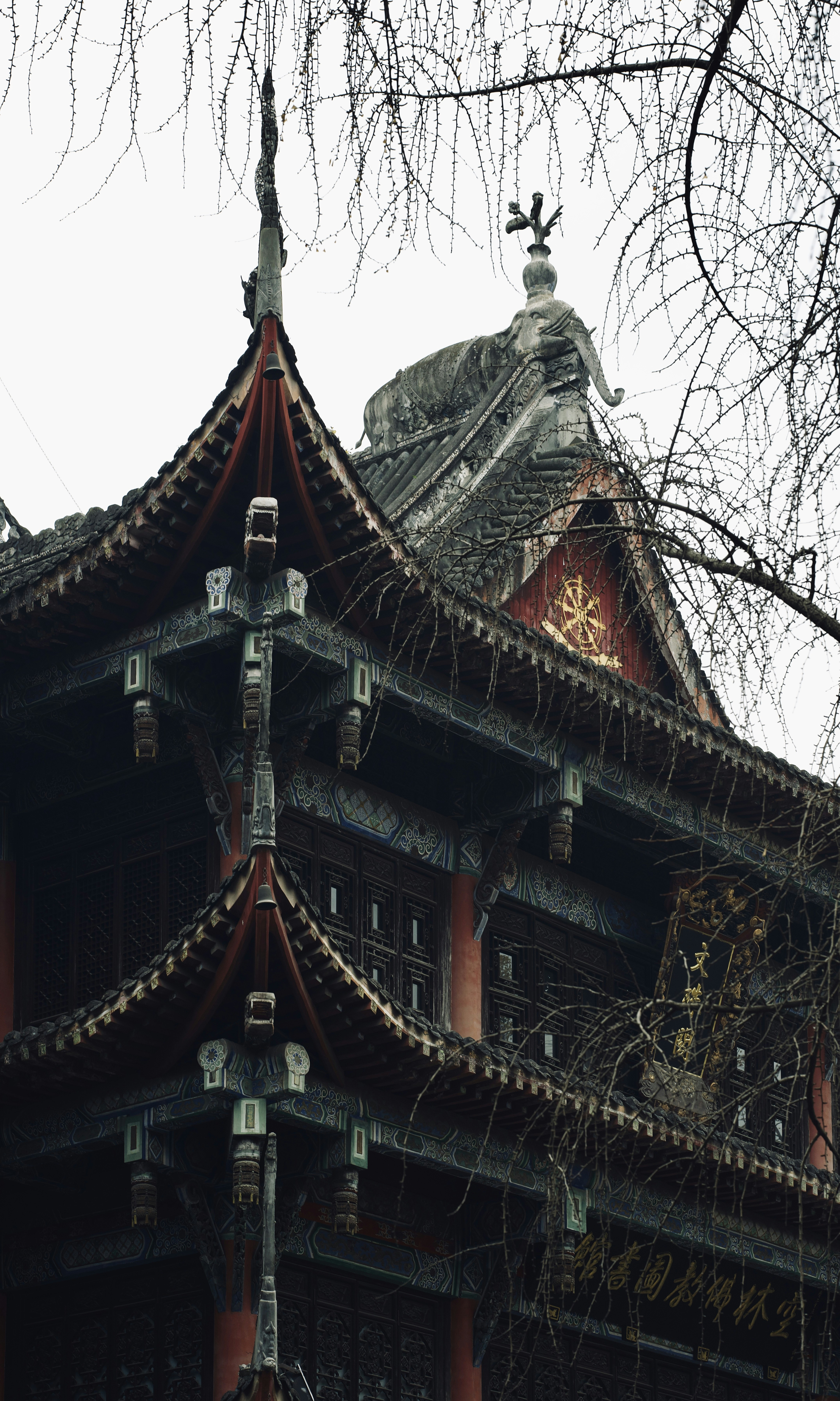 Intricate details of a traditional building's rooftop adorned with ornate carvings and a decorative finial, framed by delicate branches.