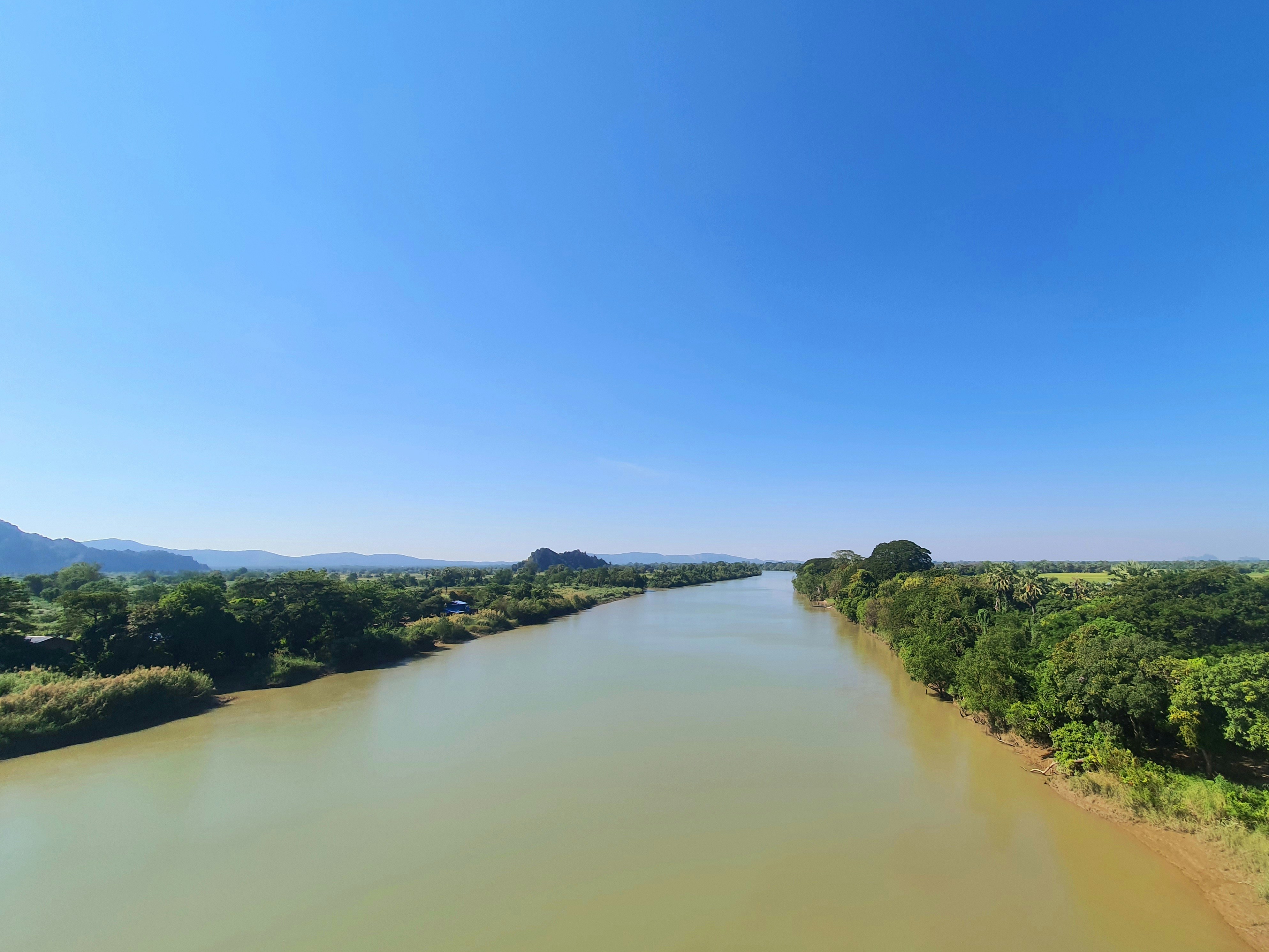 Wide river flanked by lush greenery under a clear blue sky.