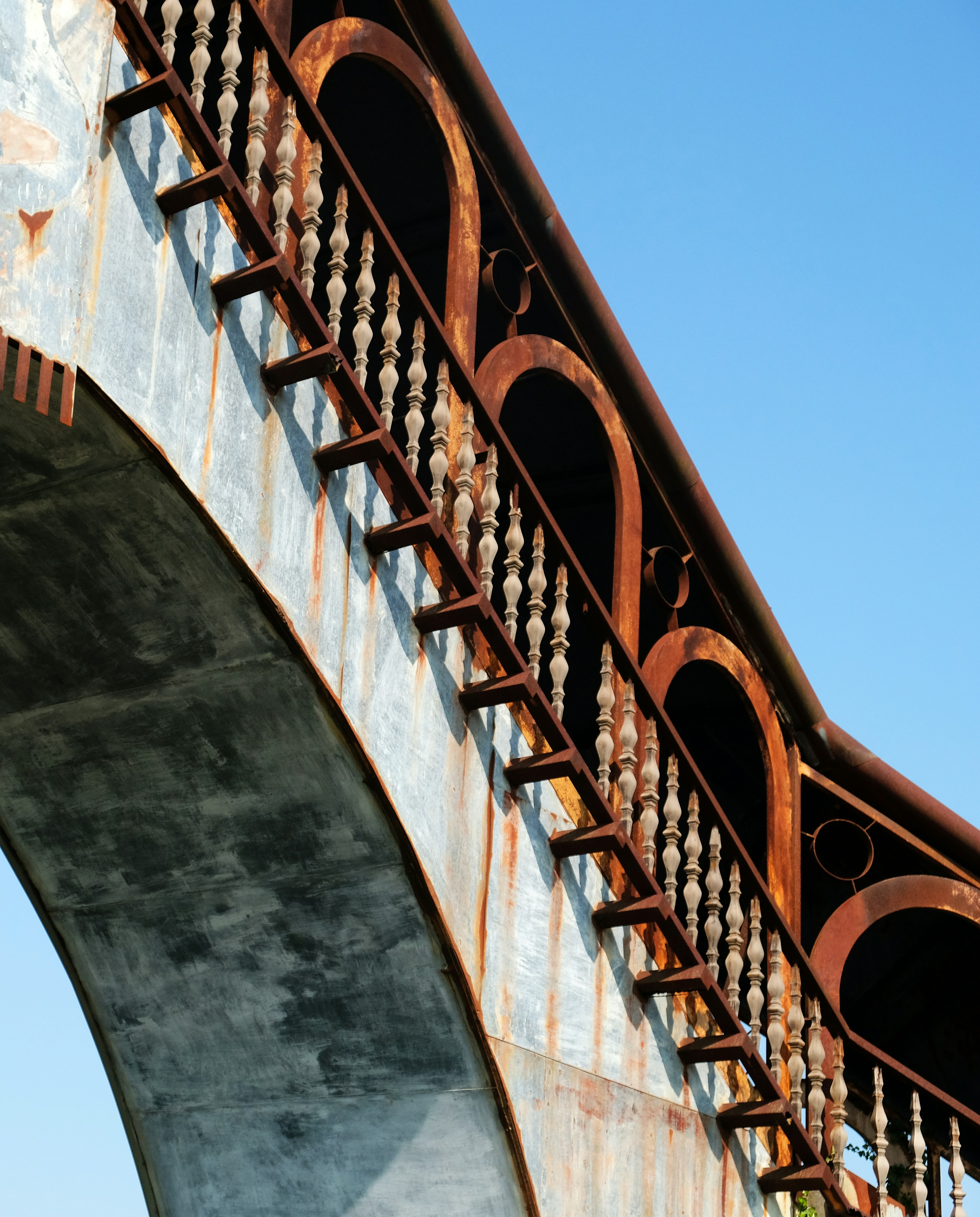 A close-up view of a weathered bridge showcasing intricate ironwork and rust details against a clear blue sky.