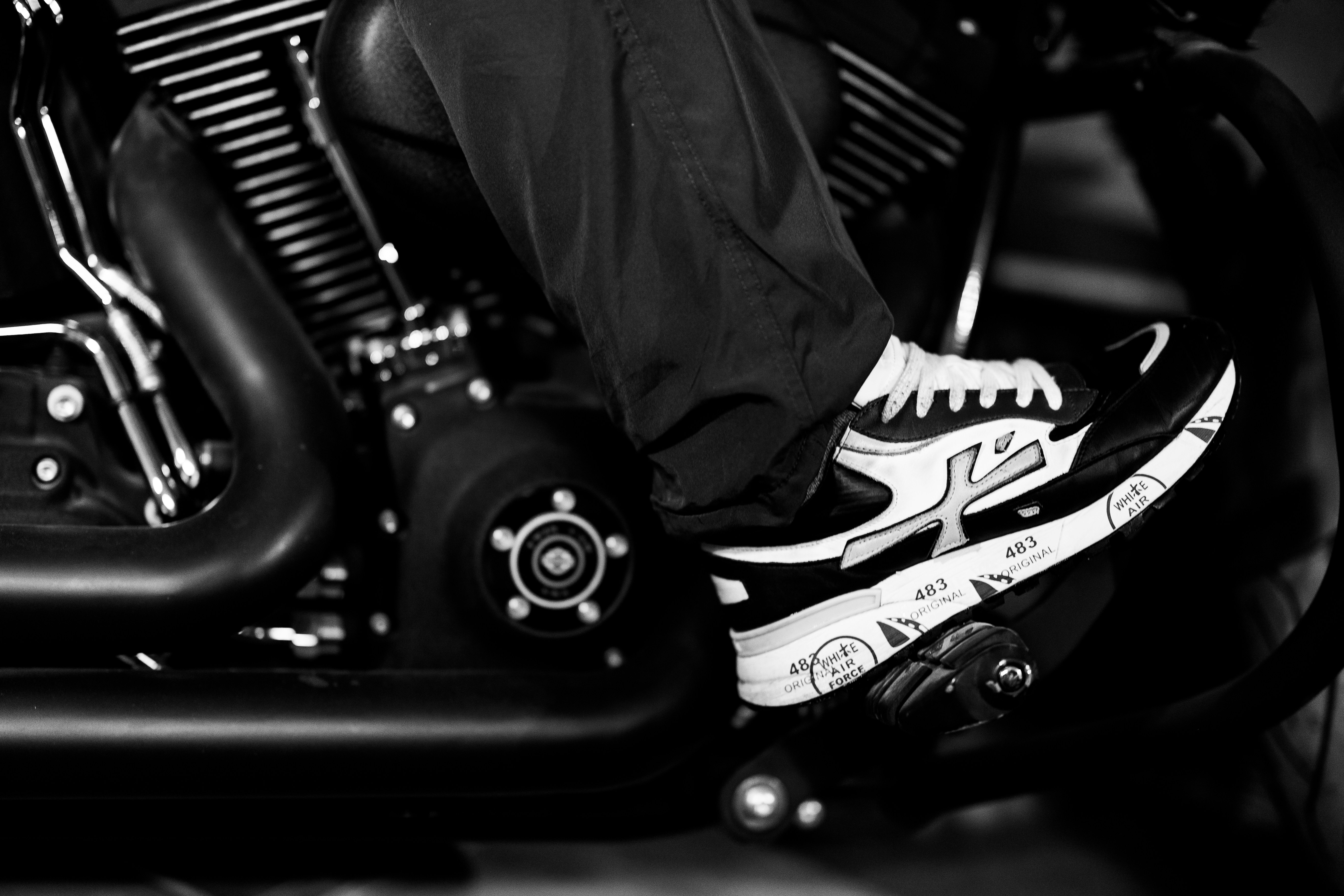 Sole Grip on Chrome: A Black-and-White Close-Up of a Rider's Foot on a Motorcycle Pedal
