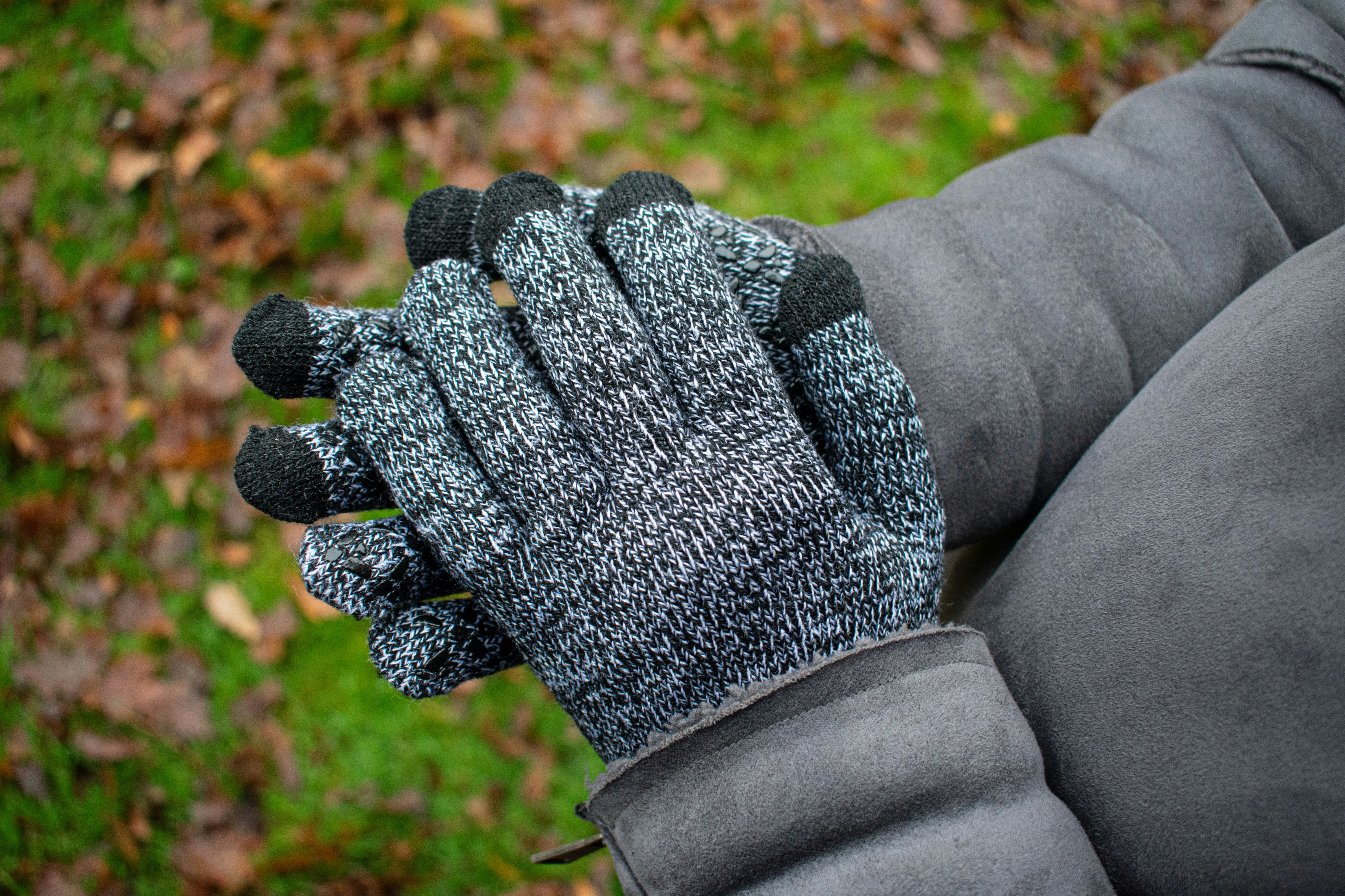 Close-up of a pair of knitted gloves resting in a person's hands, set against a backdrop of autumn leaves.
