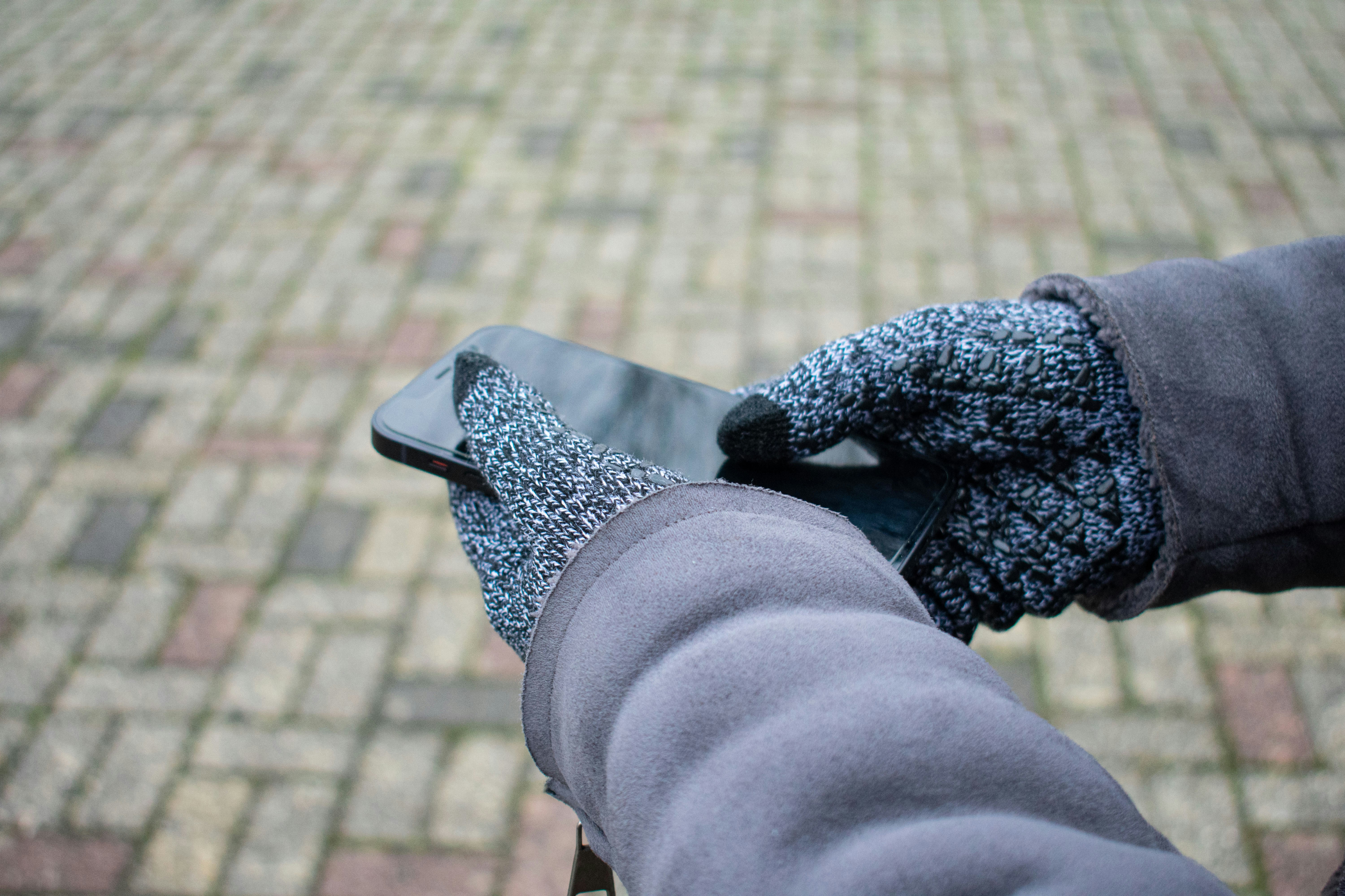 Hands clad in textured gloves interact with a smartphone on a patterned stone surface.