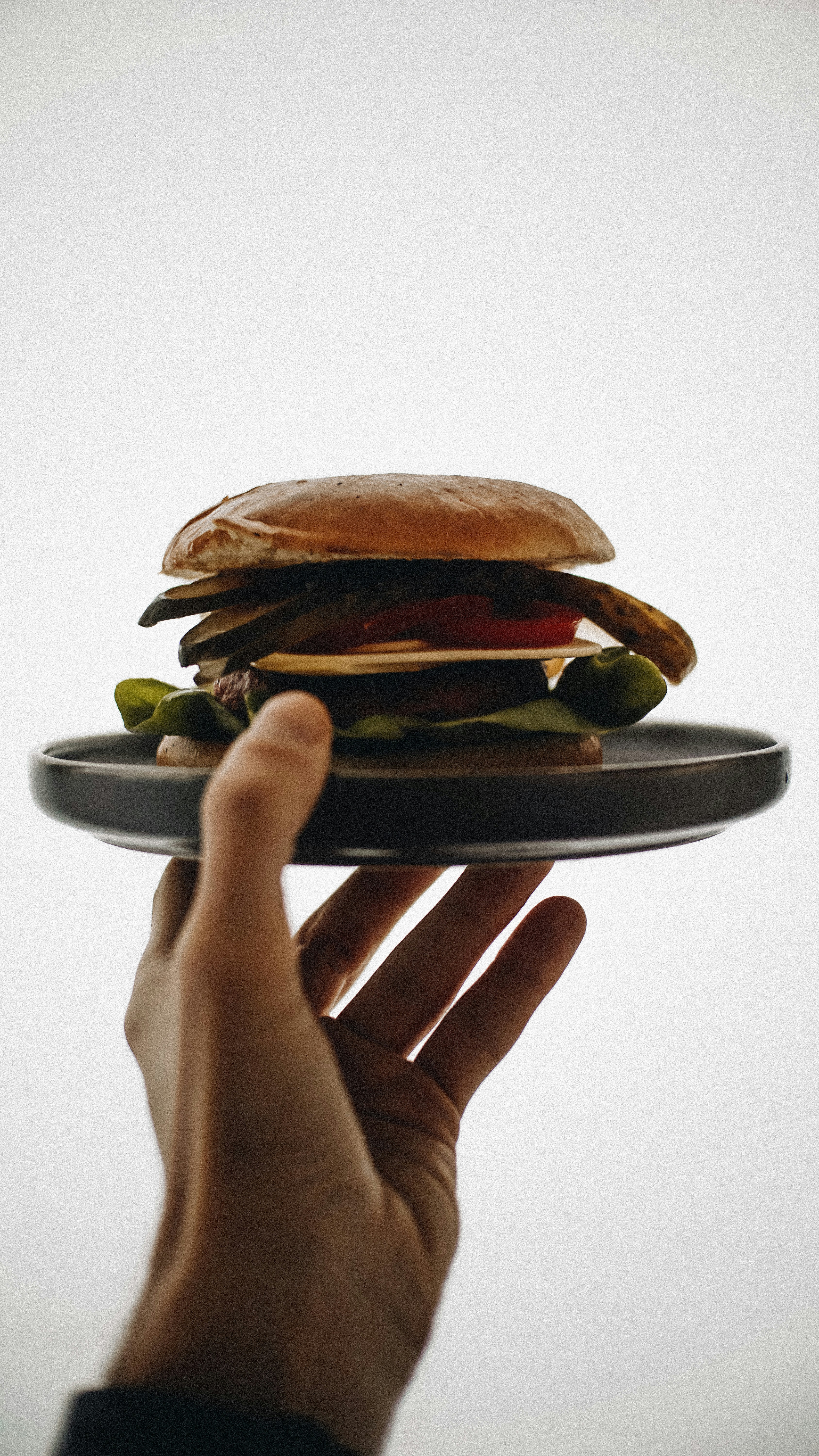 Gripped Bite: A Burger Balanced on a Plate Against a Stark White Backdrop.