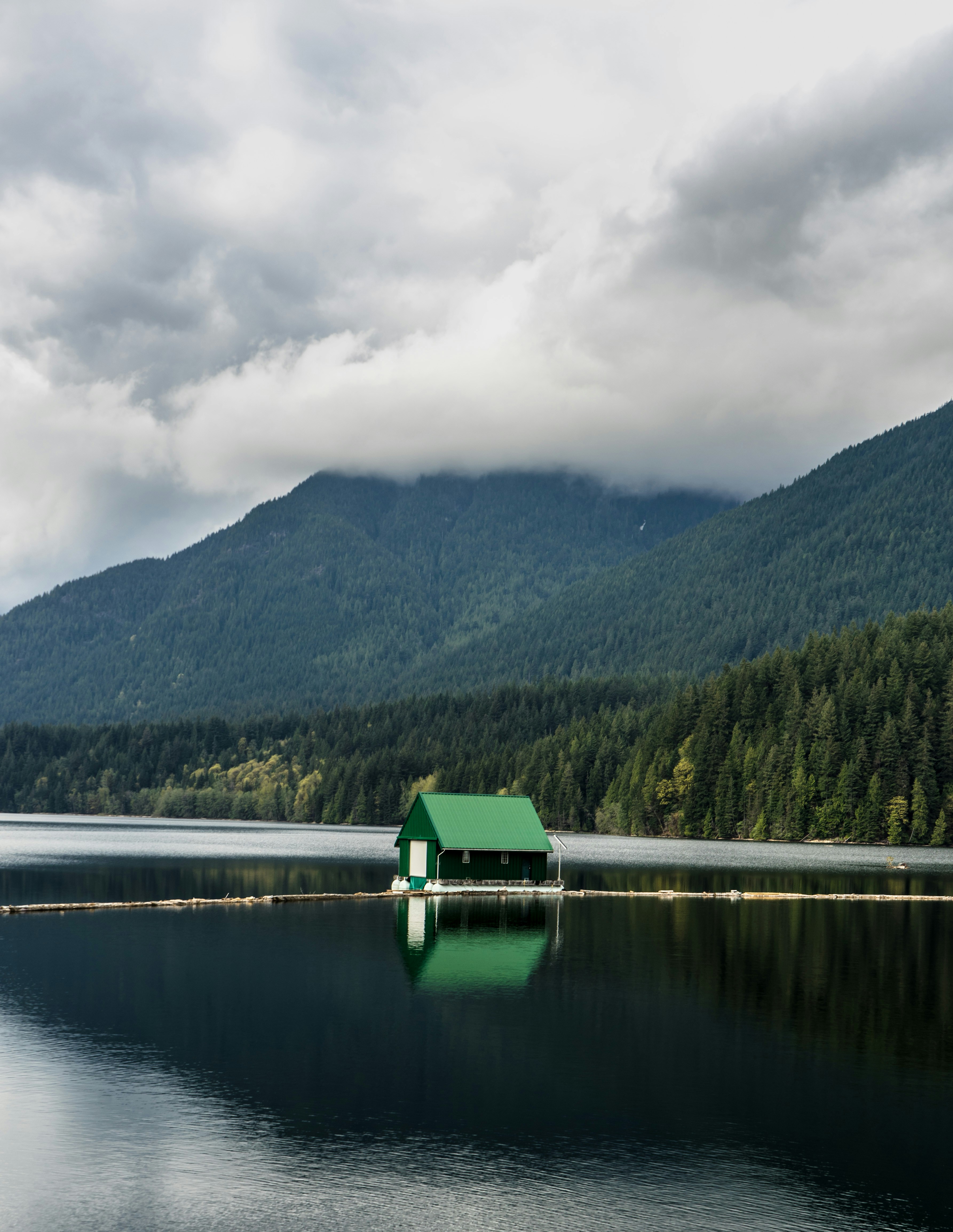 Green-roofed boathouse anchored on a glassy lake under towering pines