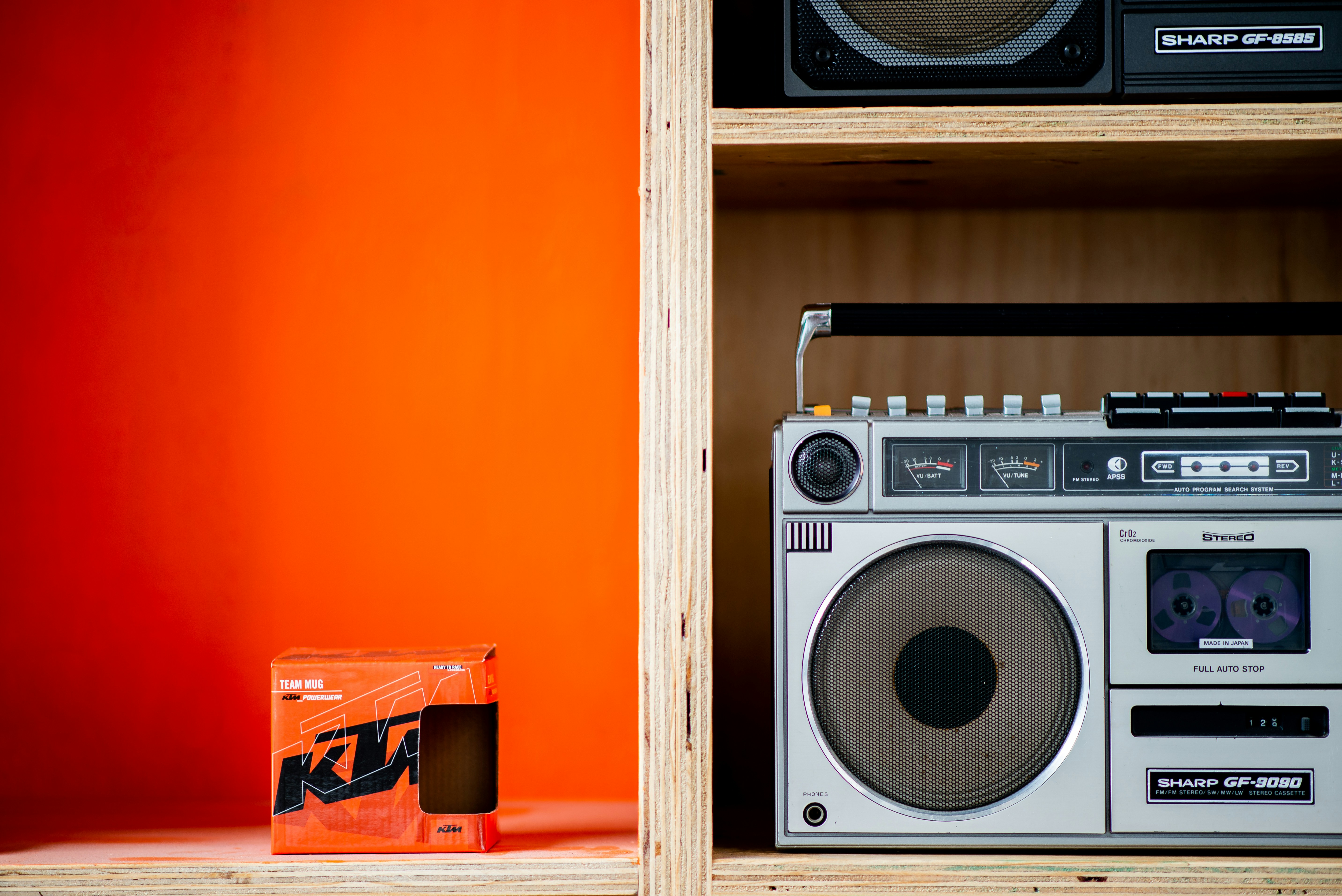 Orange background with a vintage boombox and an orange KTM box, showcasing a blend of retro aesthetics and modern design.