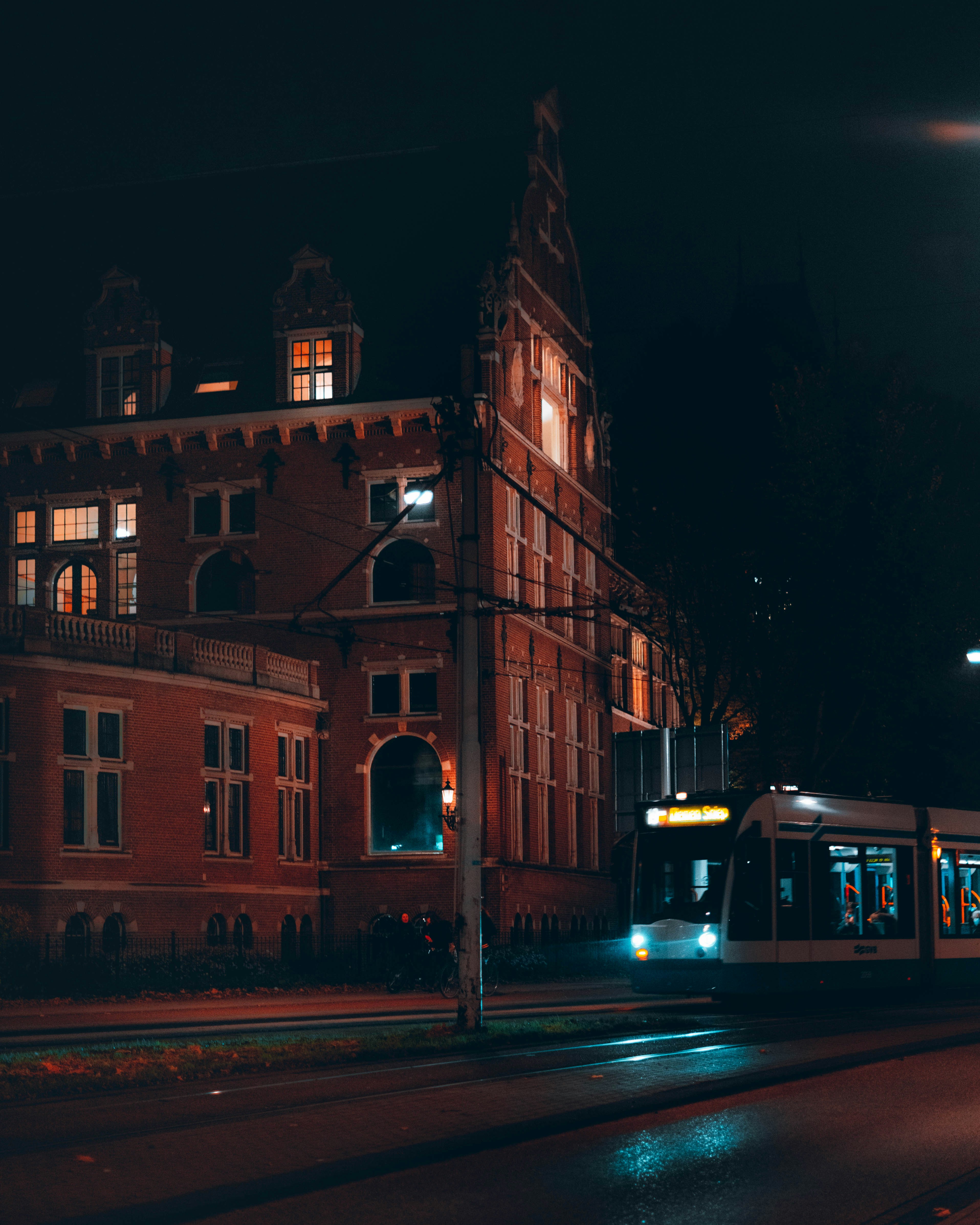 Historic building illuminated at night with a passing tram in the foreground. The architectural details are accentuated by warm lighting.