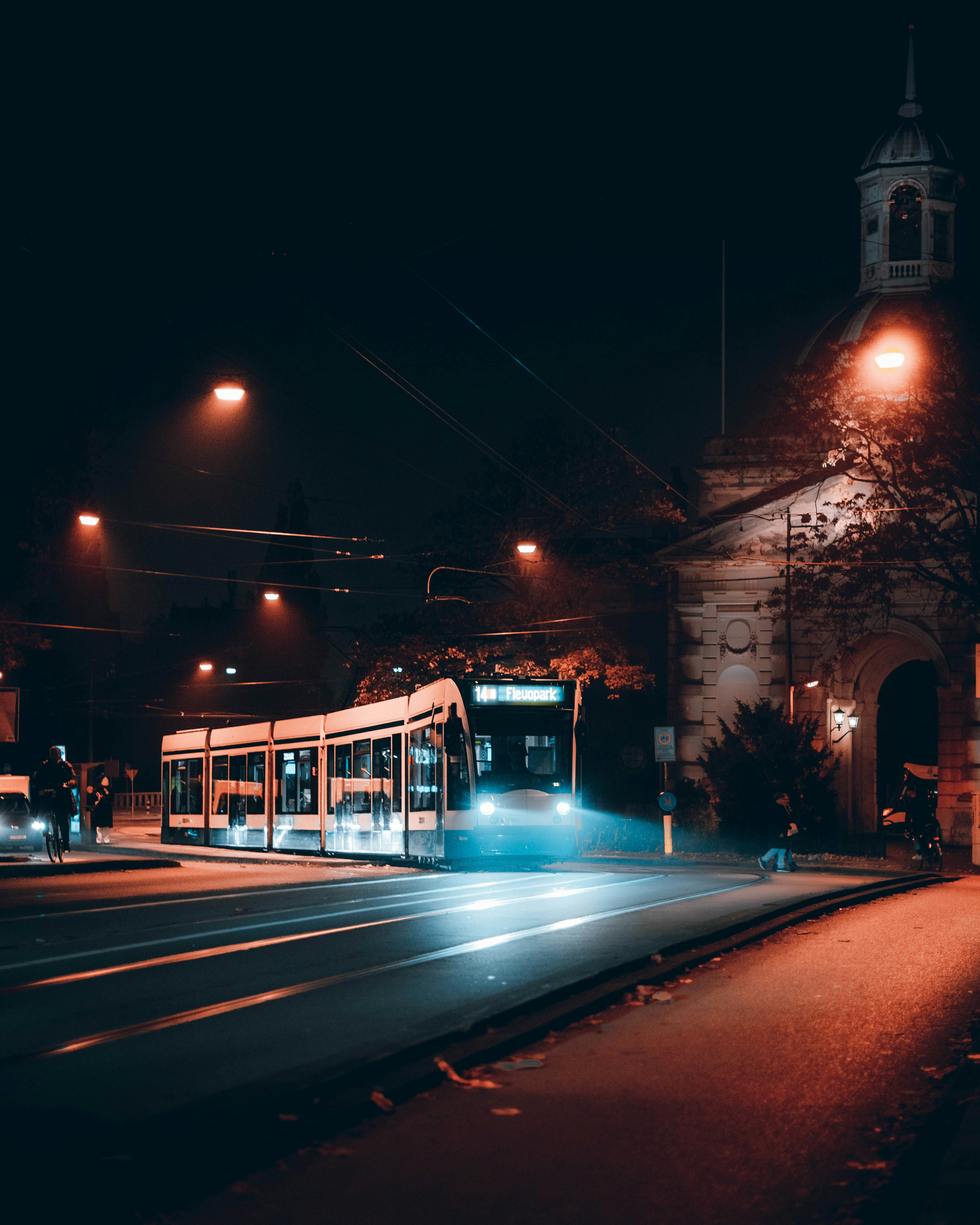 Tram gliding through a dimly lit street, illuminated by street lamps and the glow of nearby architecture.