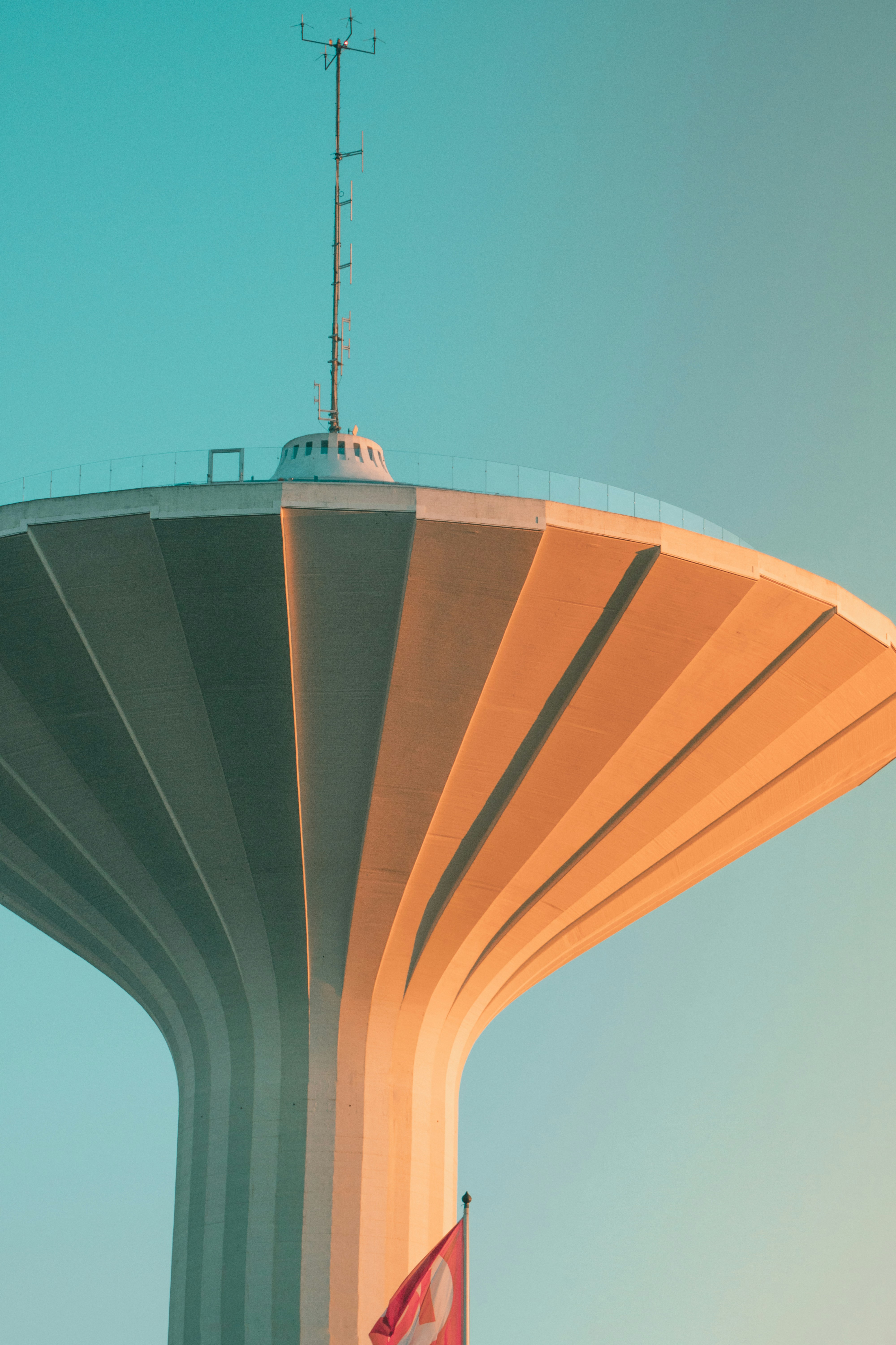 A modern water tower with a distinctive funnel shape, highlighted by warm sunlight against a clear sky.