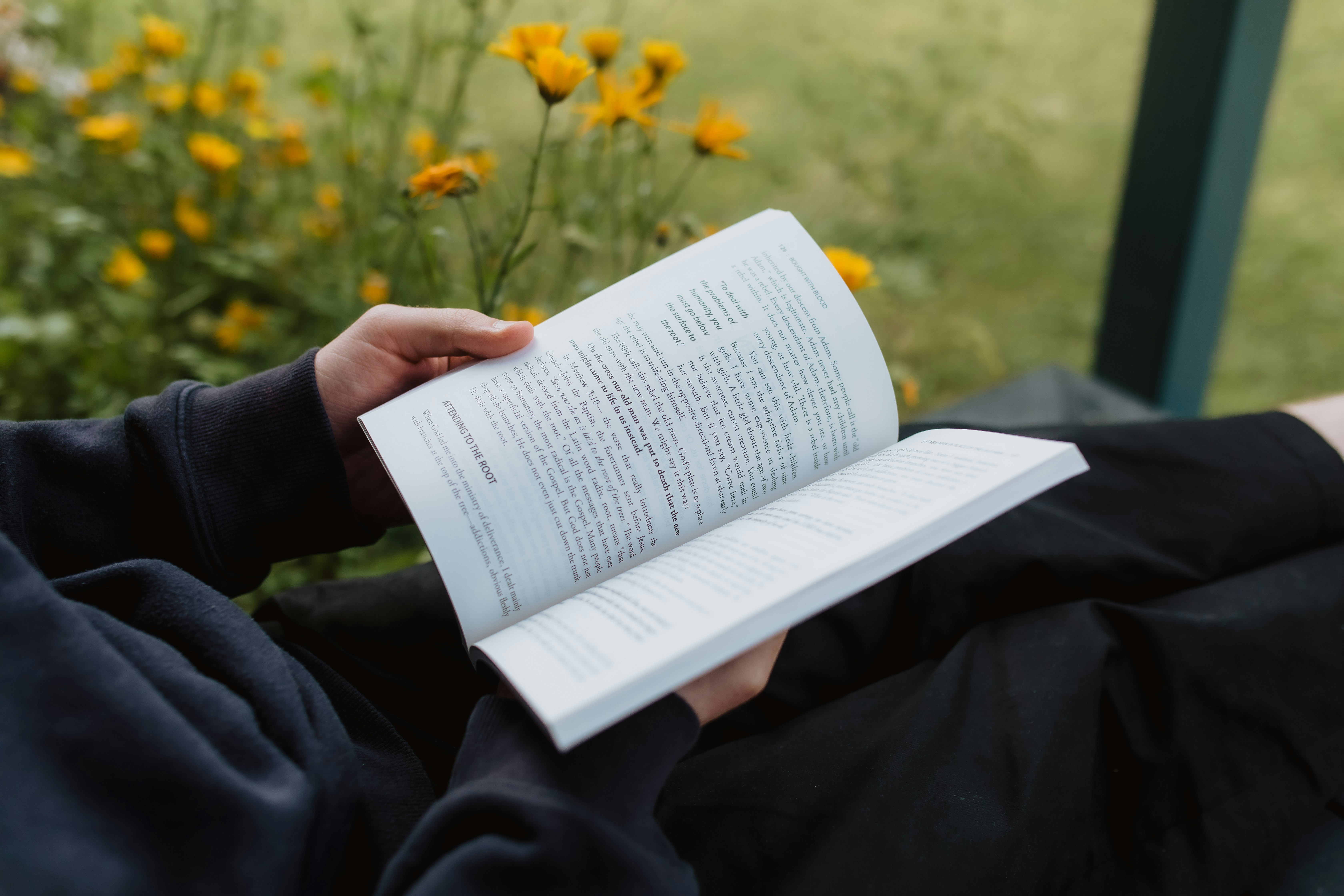 A person reading a book while seated among vibrant yellow flowers, creating a serene outdoor reading atmosphere.