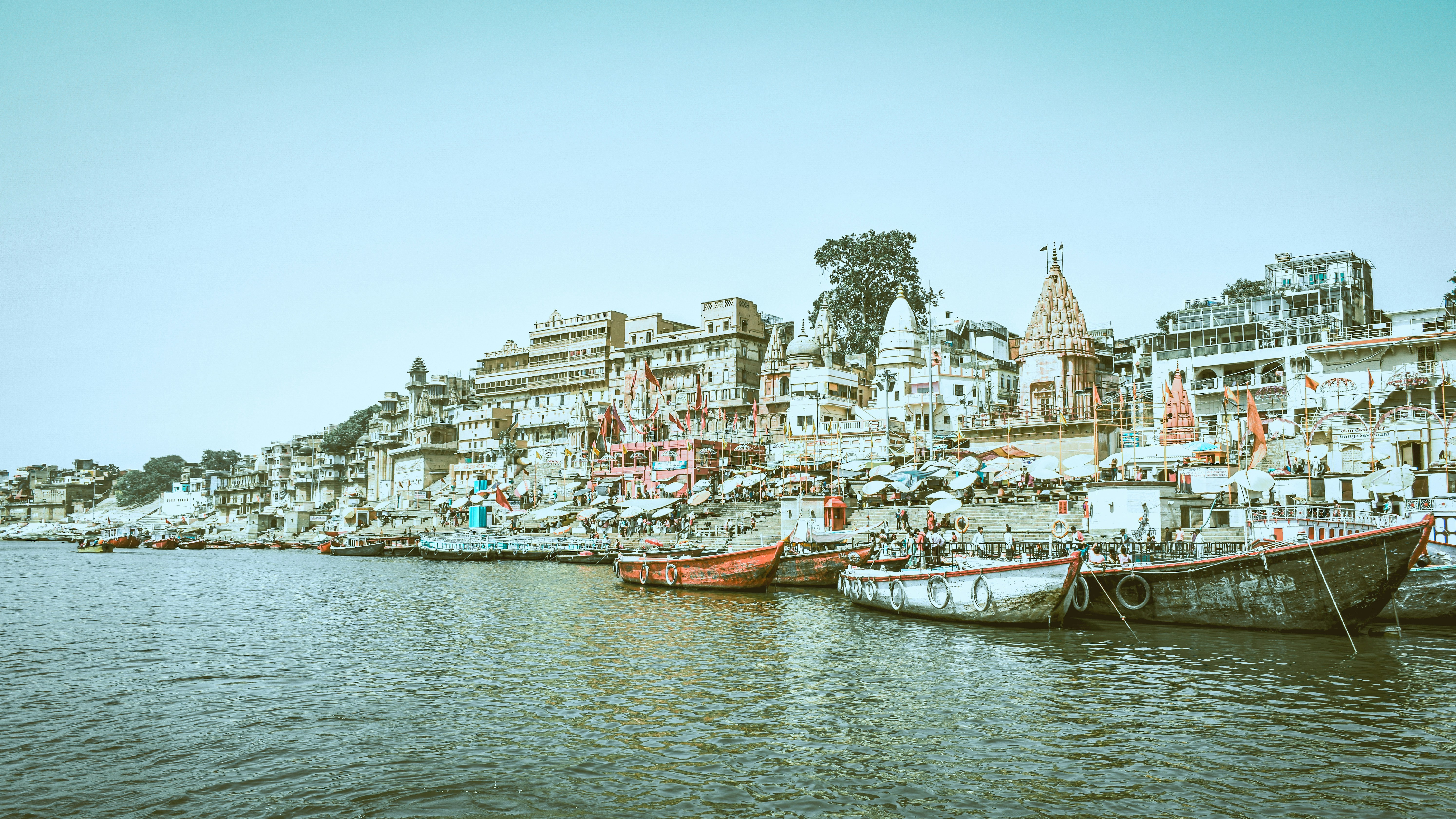Colorful boats line the tranquil riverbank, framed by a vibrant collection of temples and buildings that reflect the cultural essence of the area.