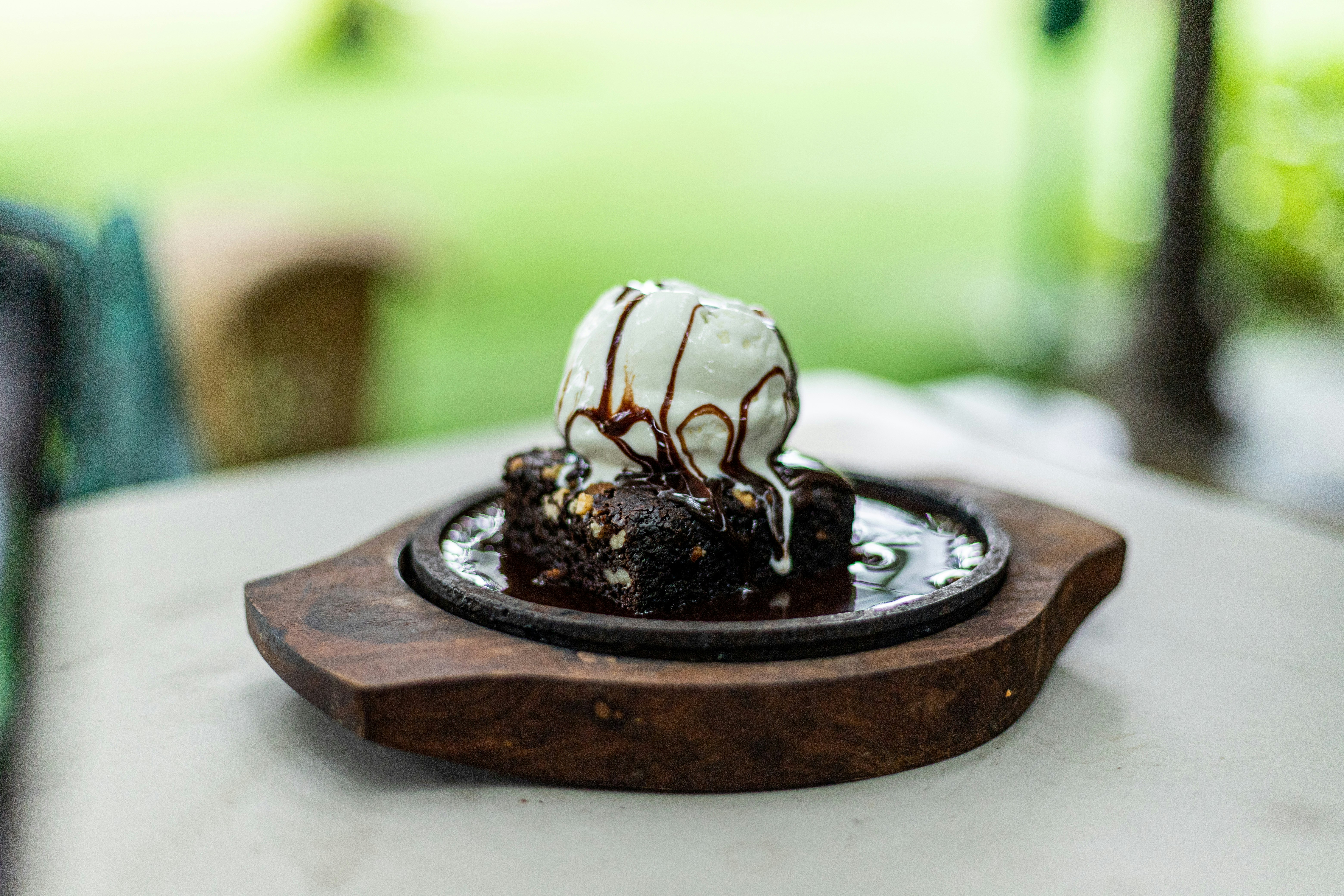 Chocolate brownie topped with vanilla ice cream and drizzled with chocolate sauce on a wooden dish.