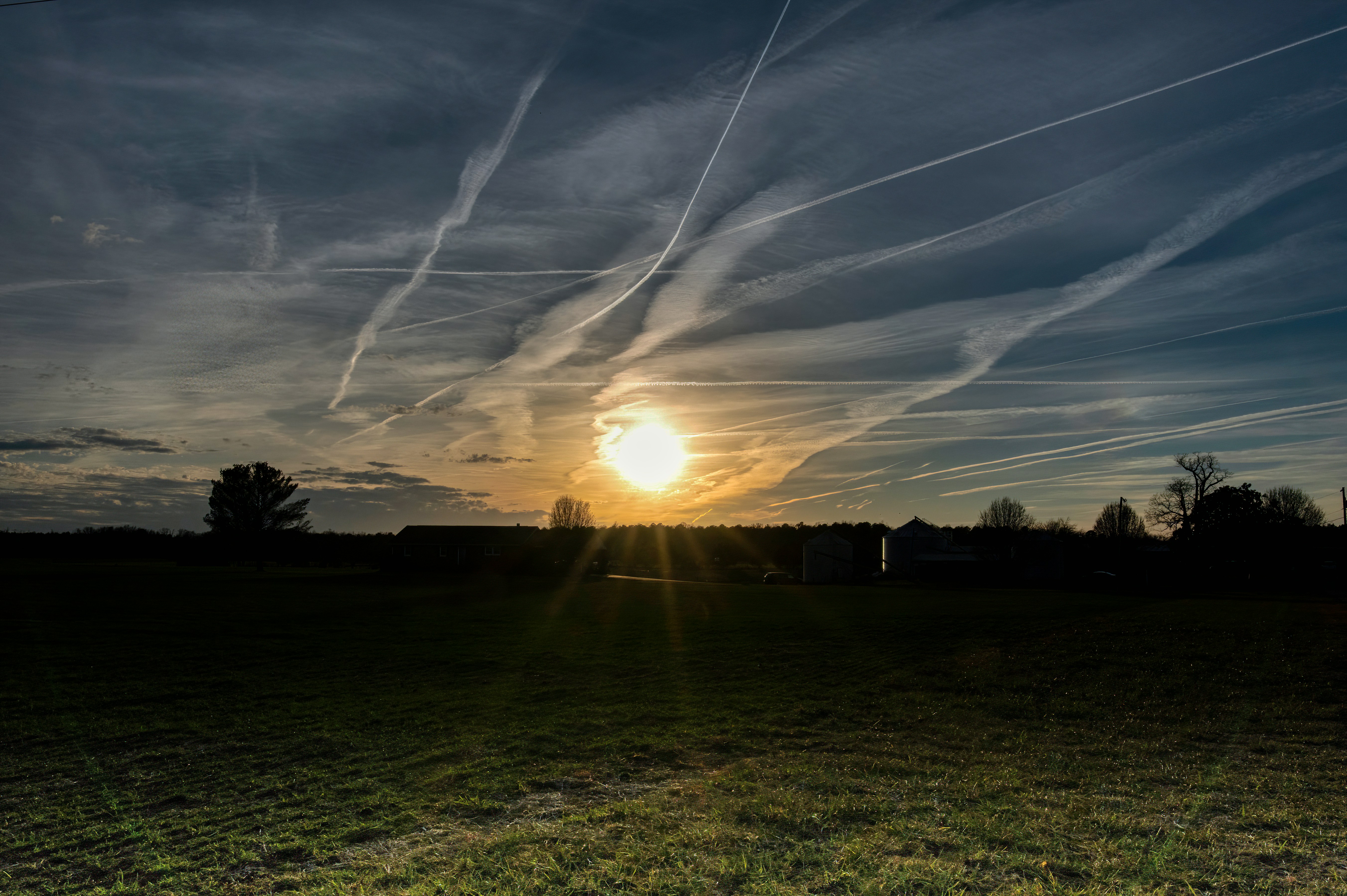 Crisscrossed Contrails Framing a Dusk Sun Over a Quiet Field