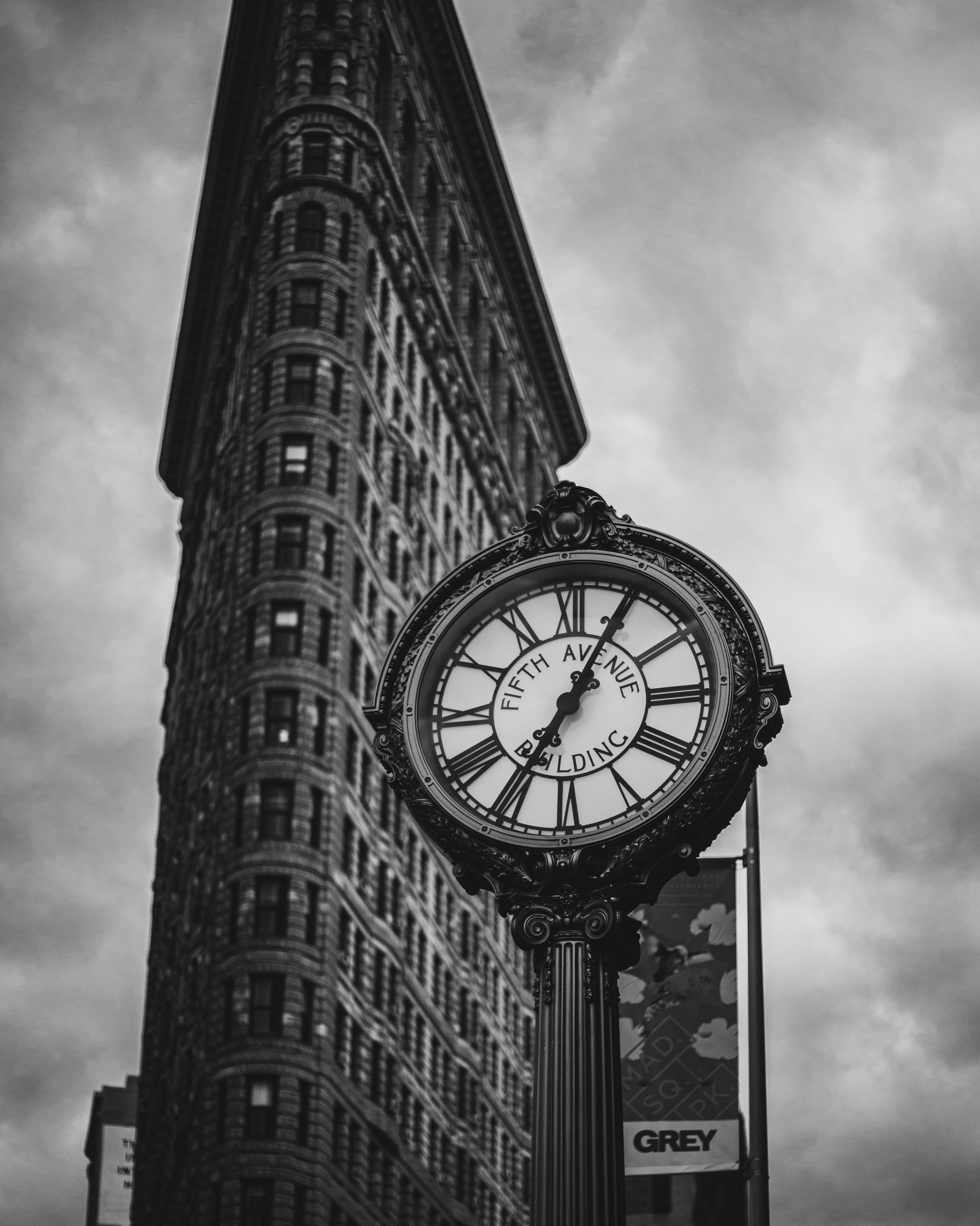 Vintage clock in front of the iconic Flatiron Building, showcasing the architectural beauty of New York City. Black and white tones enhance the historical atmosphere.