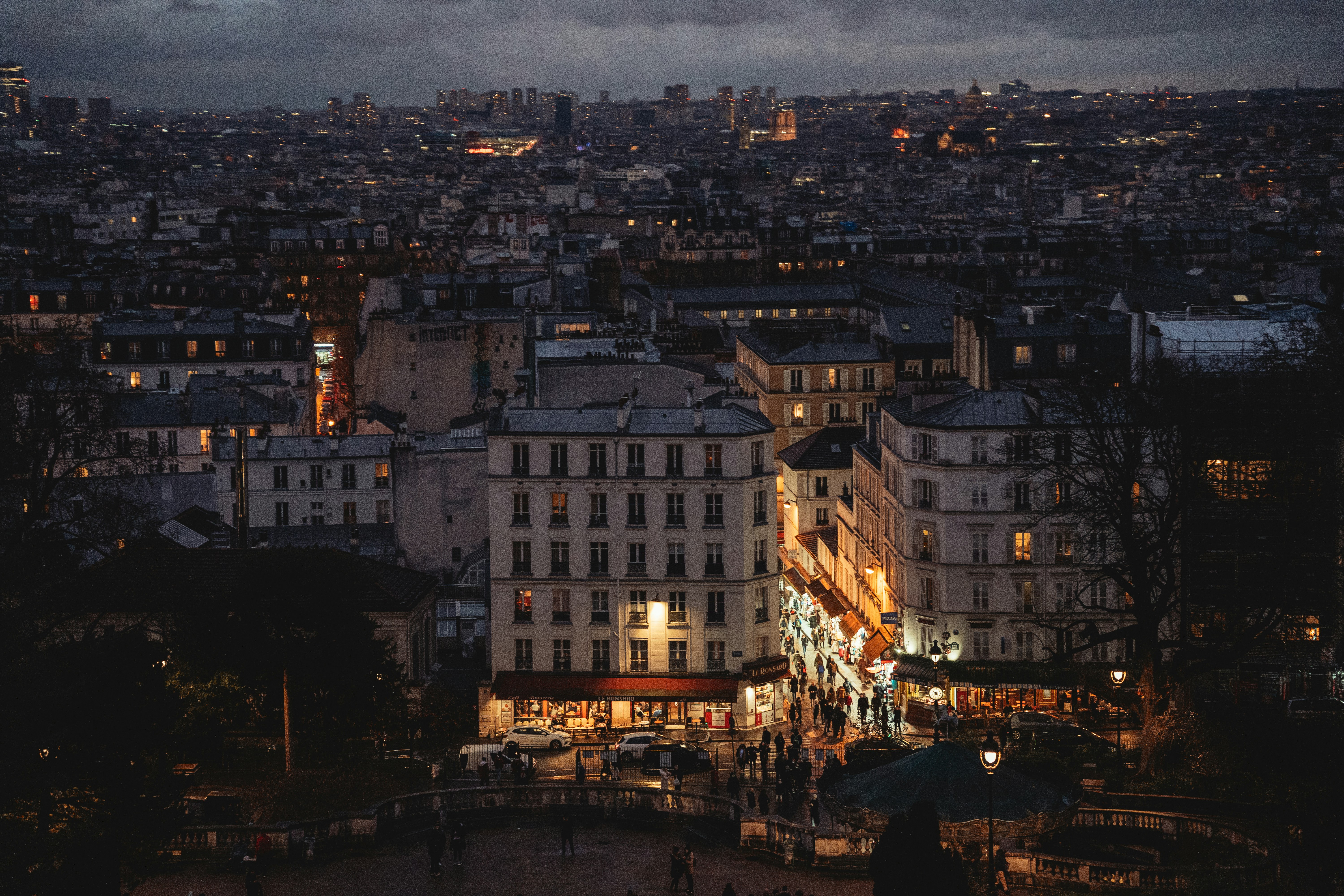 Parisian rooftops and lively streets illuminated under a moody evening sky.