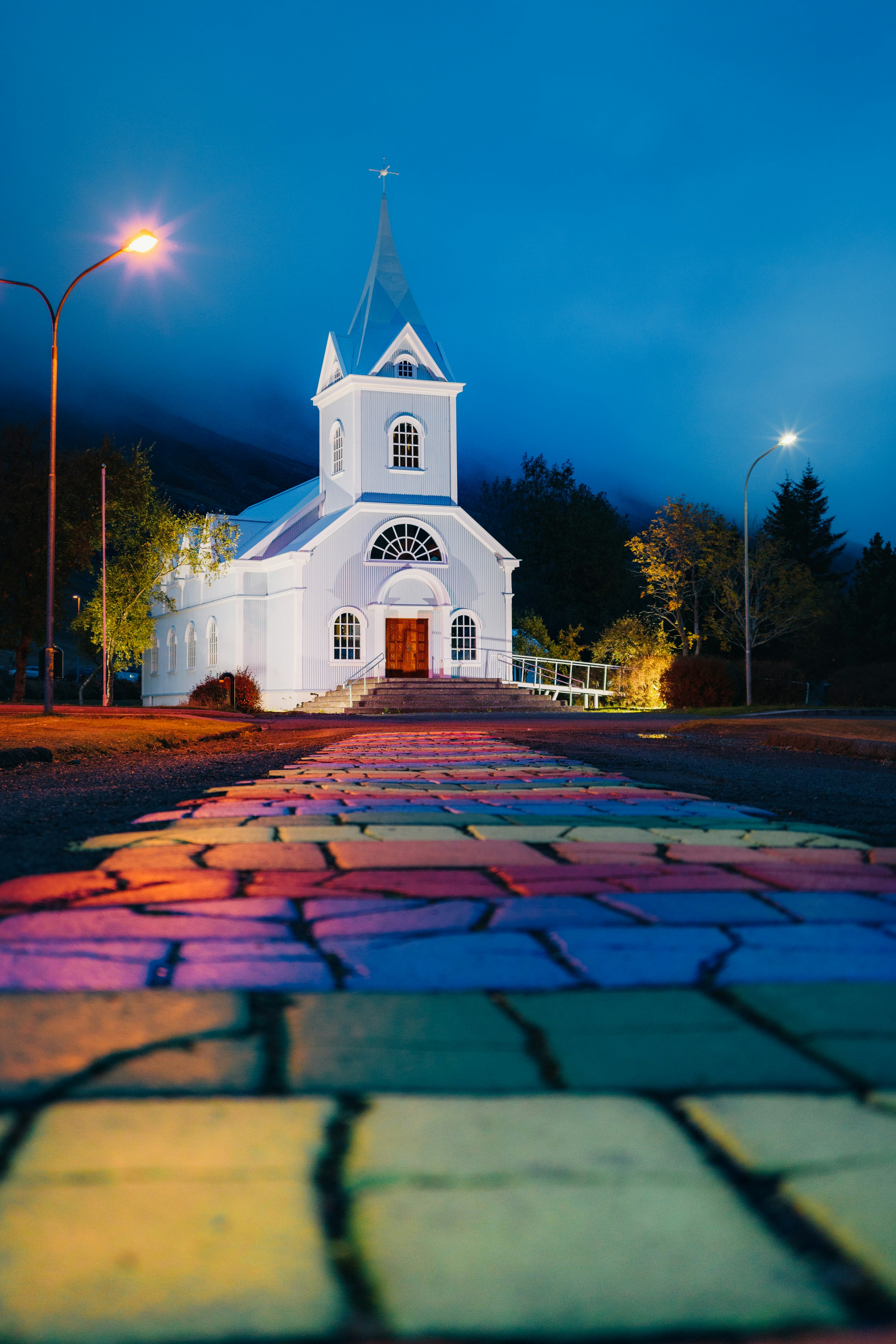 Colorful cobblestone path leading to a white church under a twilight sky, illuminated by streetlights. 