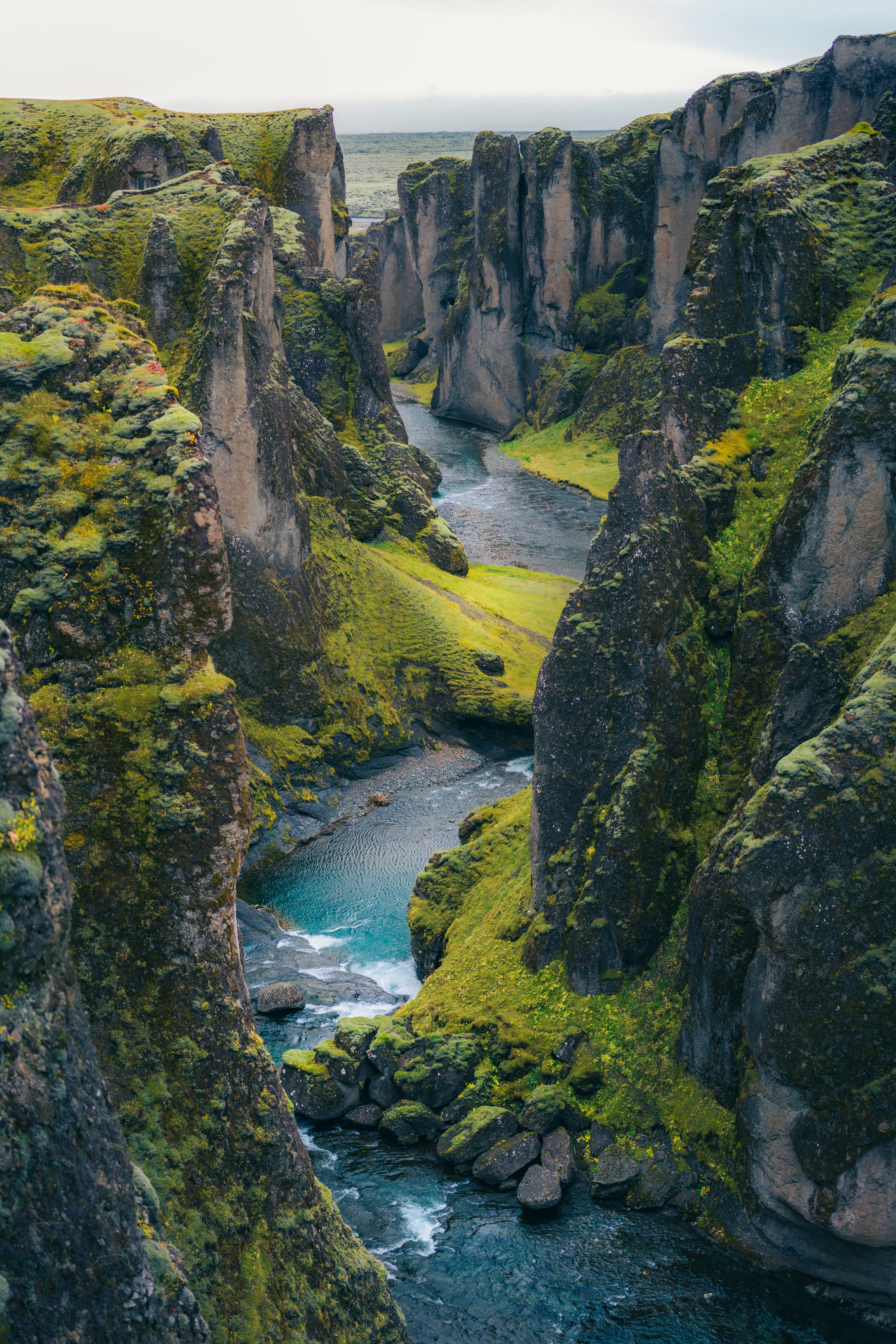 Lush green cliffs frame a winding river, showcasing the intricate beauty of a canyon landscape. Moss-covered rock formations rise dramatically from the water's edge.